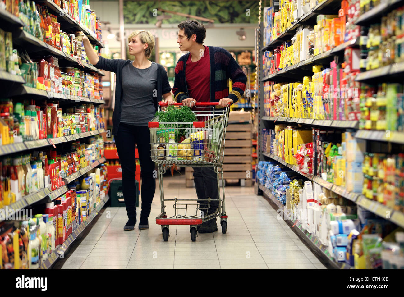 Ein junges Paar in einem großen Supermarkt, mit einem Wagen, zu Fuß ...