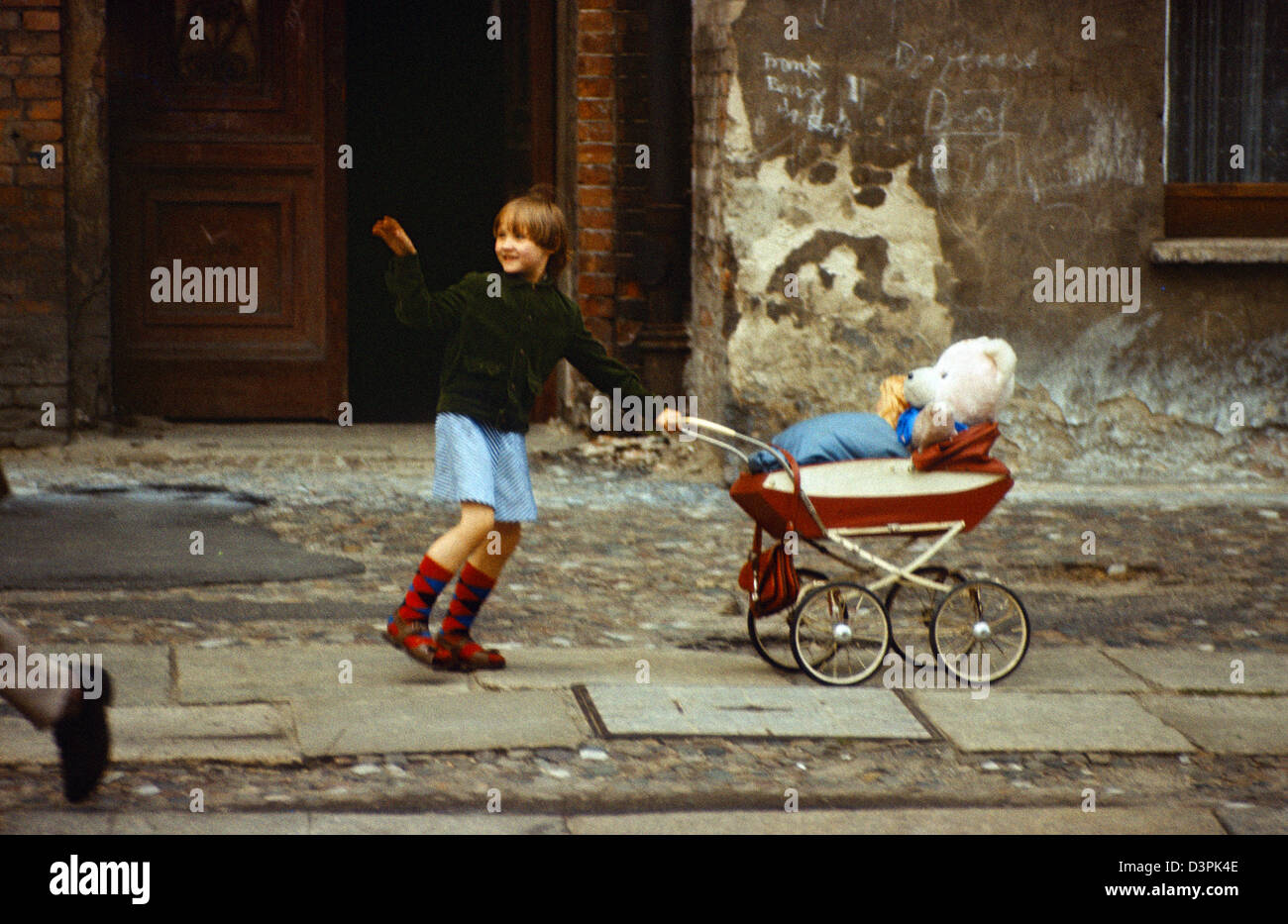 Berlin, DDR, Mädchen schiebt ihr Teddy Bär in einem Kinderwagen entlang ...