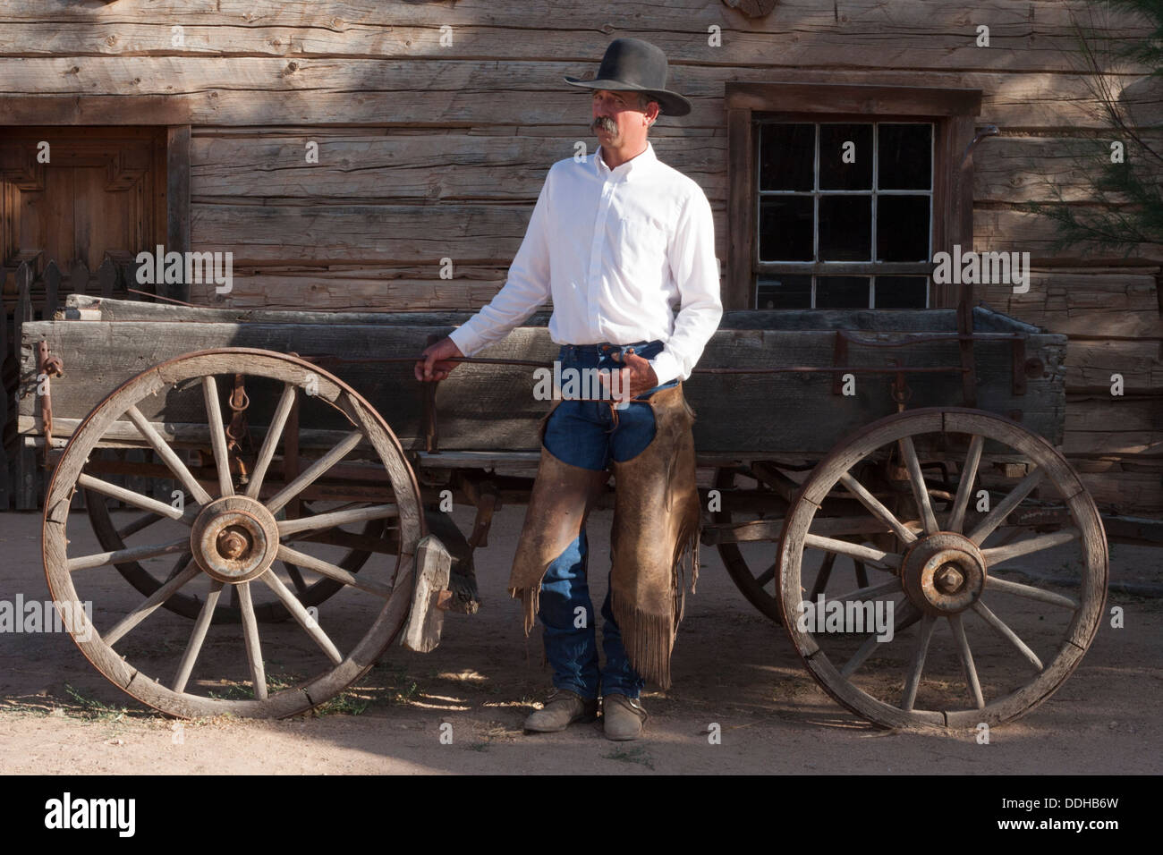 Cowboy, der vor einem alten Westernwagen und einer Scheune steht, trägt ...