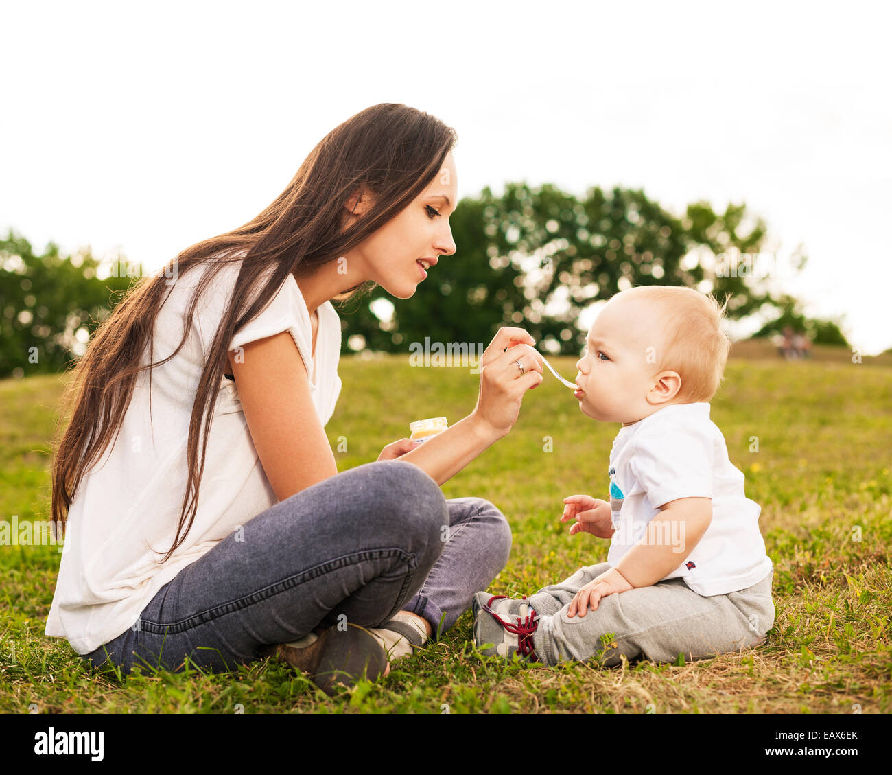 Yong-Mutter mit langen Haaren, die ihr Baby füttern pürieren im Freien ...