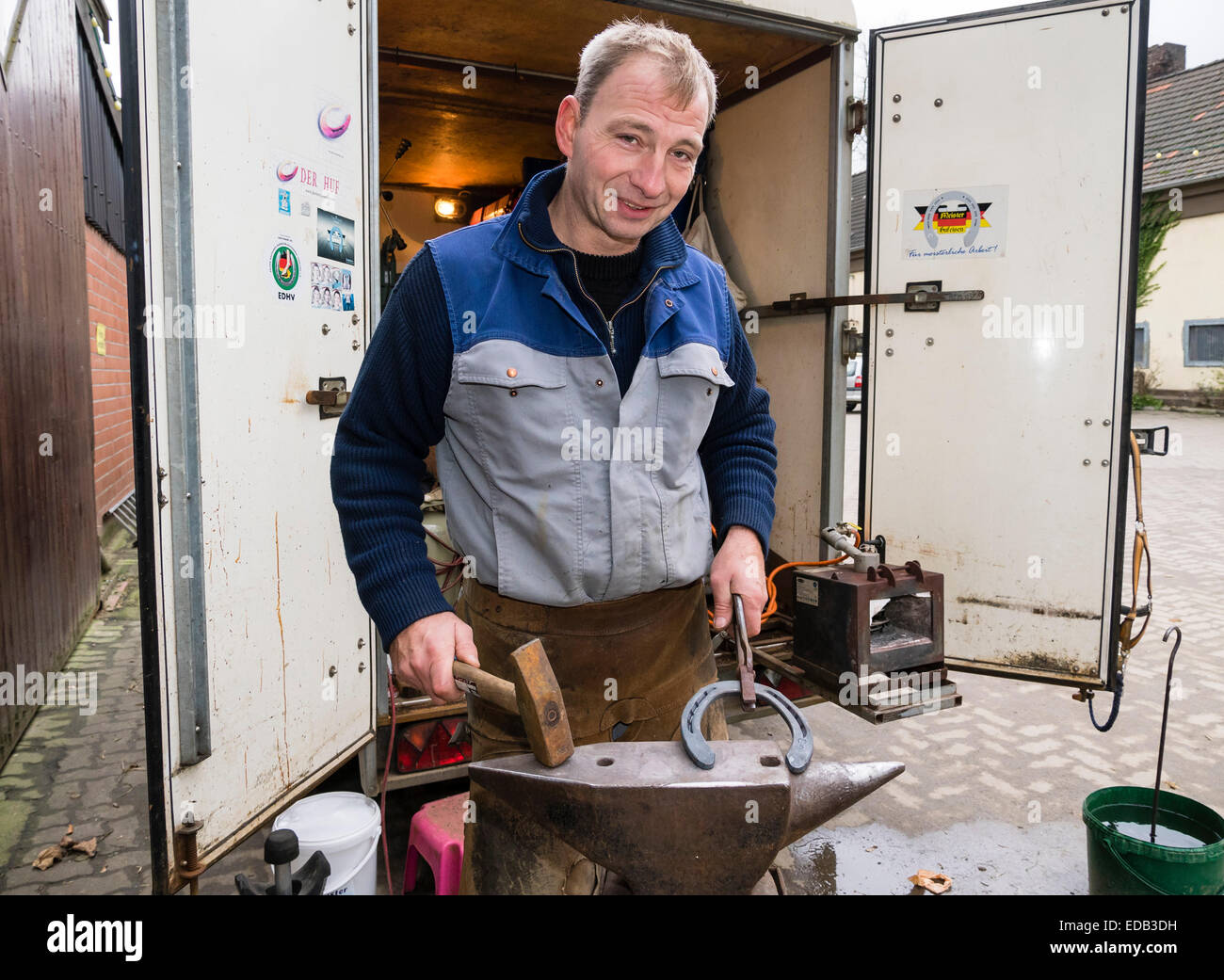 Ein Hufschmied arbeitet ein Hufeisen mit einem Hammer auf einen Amboss ...