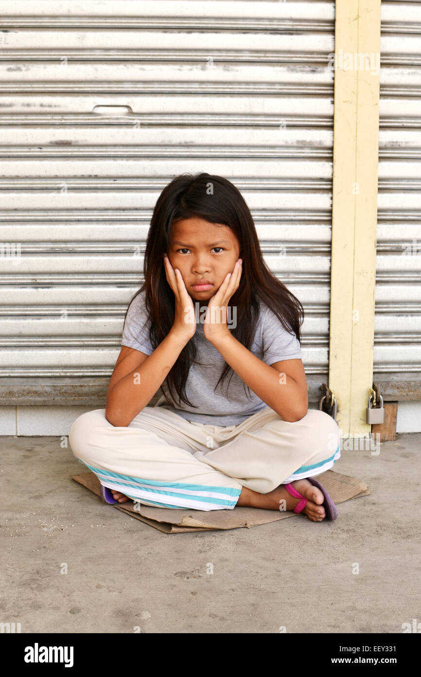 Niedliche obdachlos traurig Kind sitzt auf der Straße über einen Karton ...
