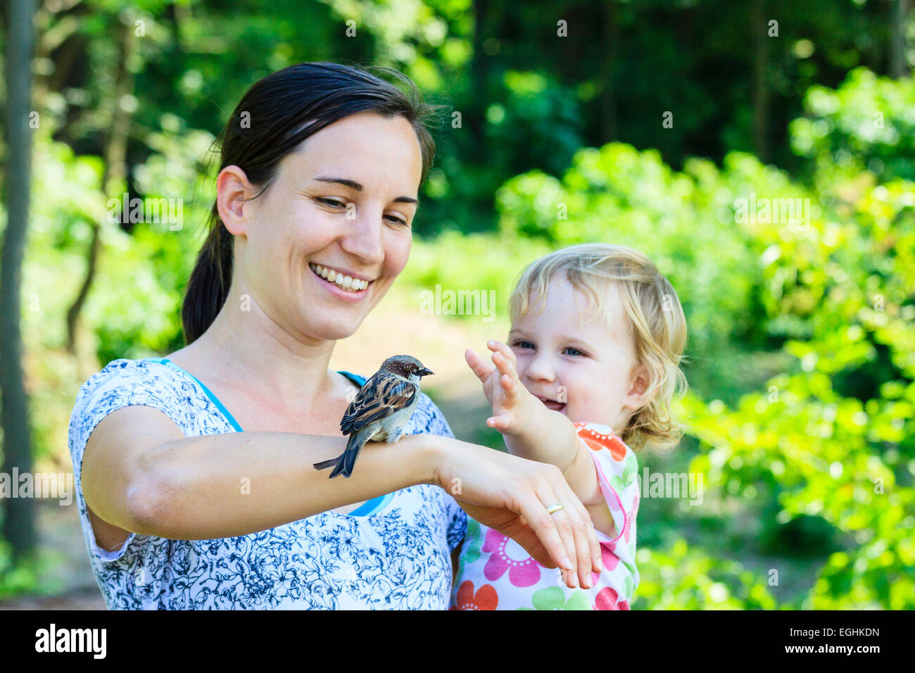 Junge Mutter und ein Kleinkind, ein Spatz thront auf der Mutter Arm ...
