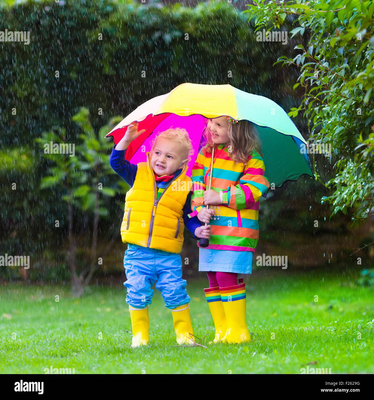 Kleine Mädchen und Jungen mit bunten Regenschirm im Regen zu spielen ...