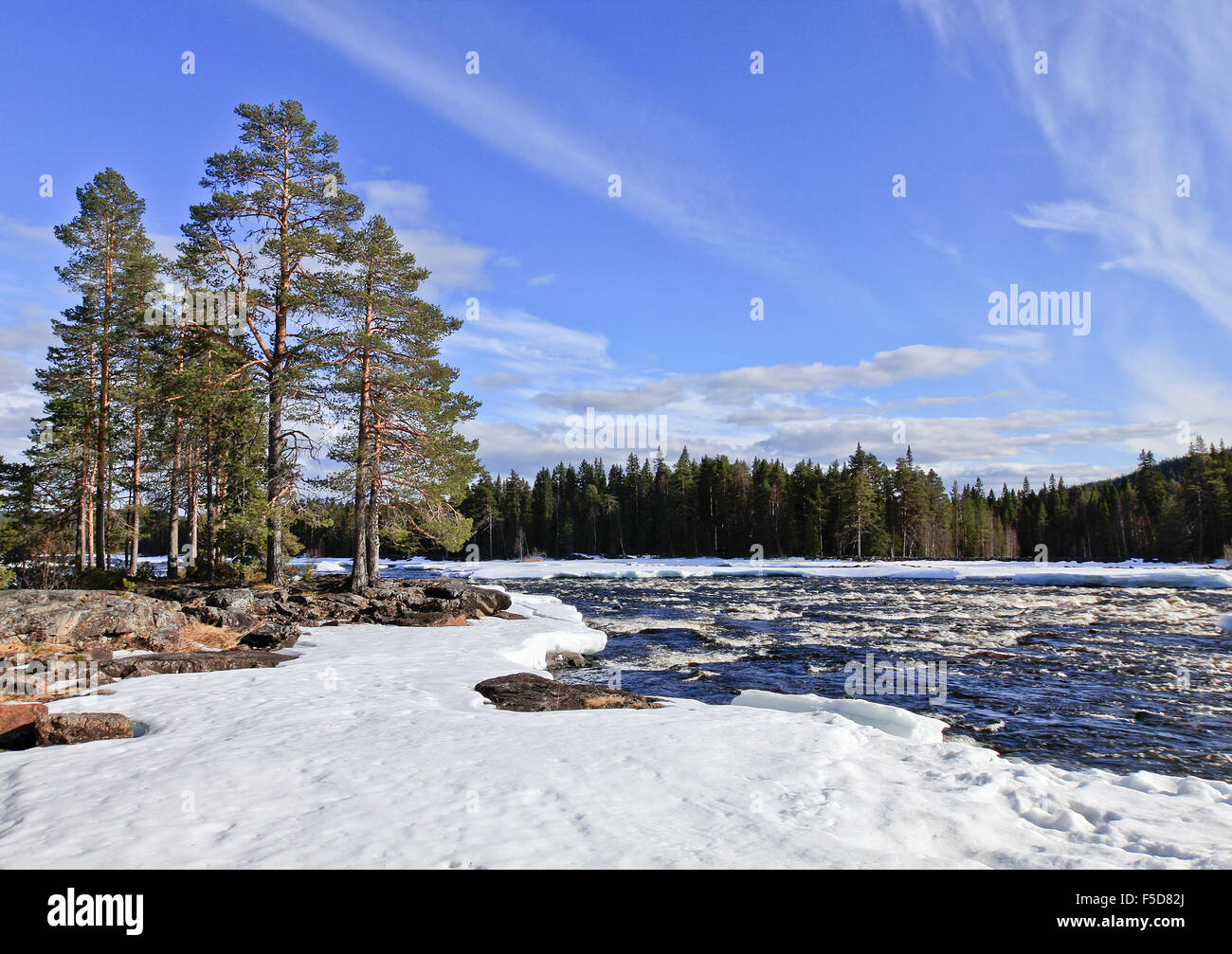 Blick auf einen Fluss im Frühling bei strahlendem Sonnenschein. Schnee ...