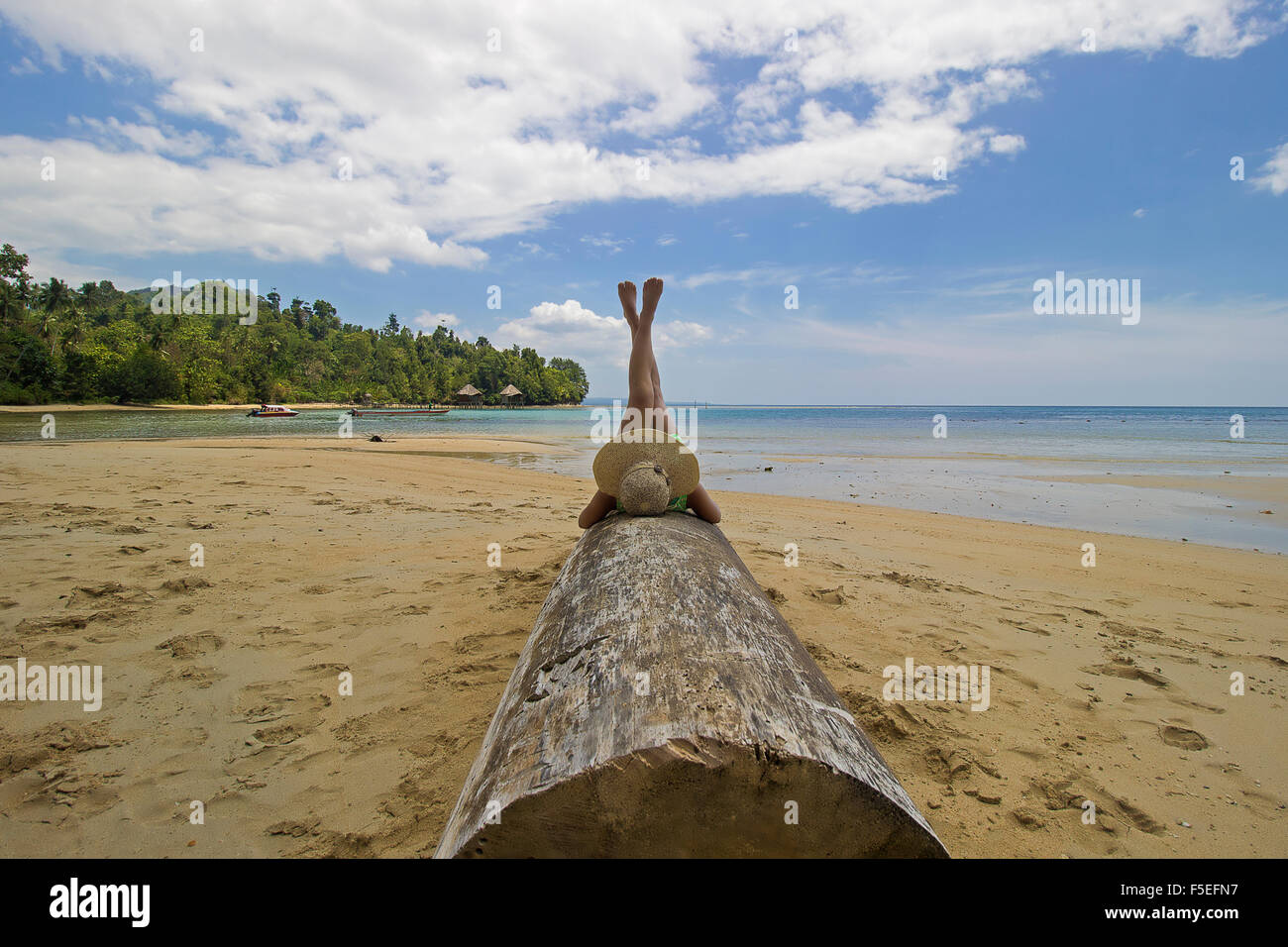 Frau liegend auf einem Baumstamm am Strand mit den Beinen in der Luft ...