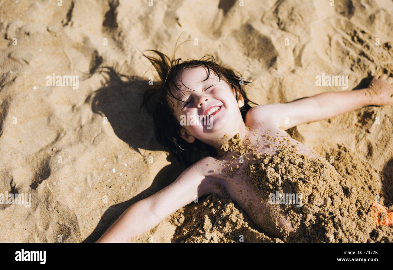 Ein Junge auf dem Rücken am Strand liegend, seinen Oberkörper mit Sand ...