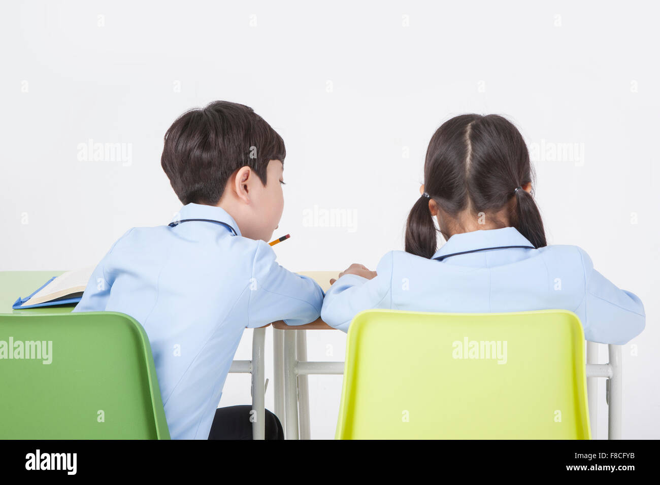 Hinteren Aussehen der Grundschule jungen und Mädchen in Schuluniformen sitzt am Schreibtisch und ...