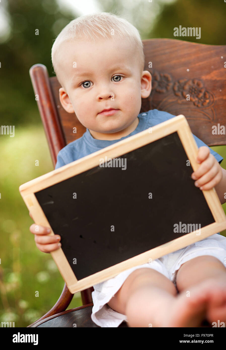 Niedliche kleine Junge mit kleinen Tafel sitzen auf Stuhl auf Wiese ...