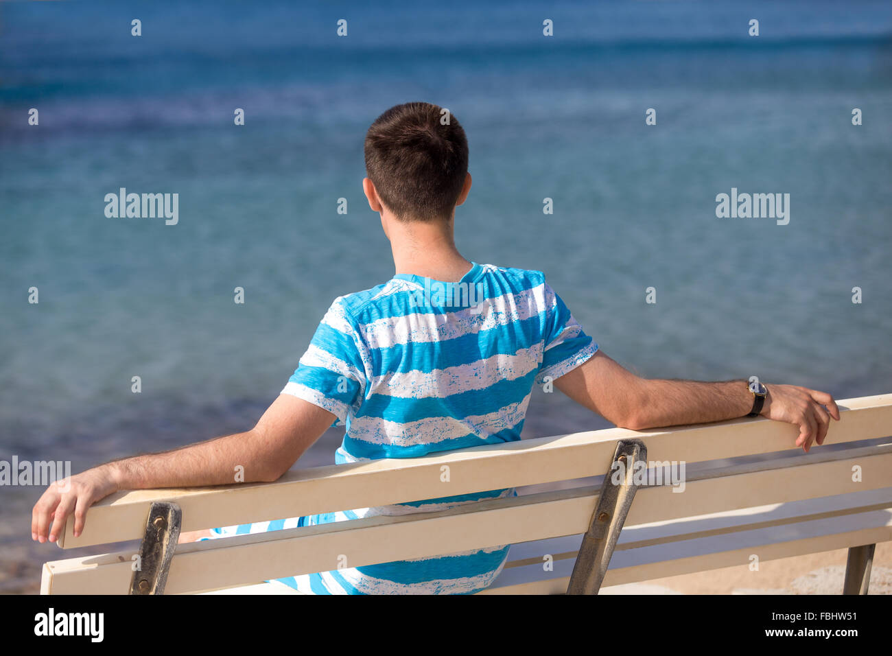 Junger Mann sitzen in bequemen Pose auf weißen Holzbank am sonnigen ...