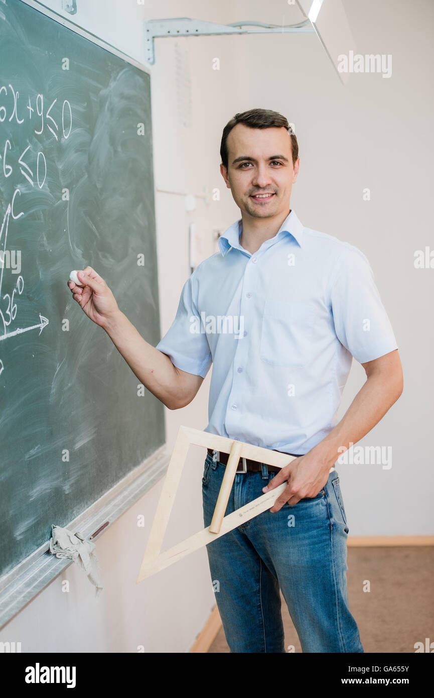 Junge Lehrer oder Schüler halten Dreieck auf Tafel mit Formel zeigen, auf die Kamera und ...