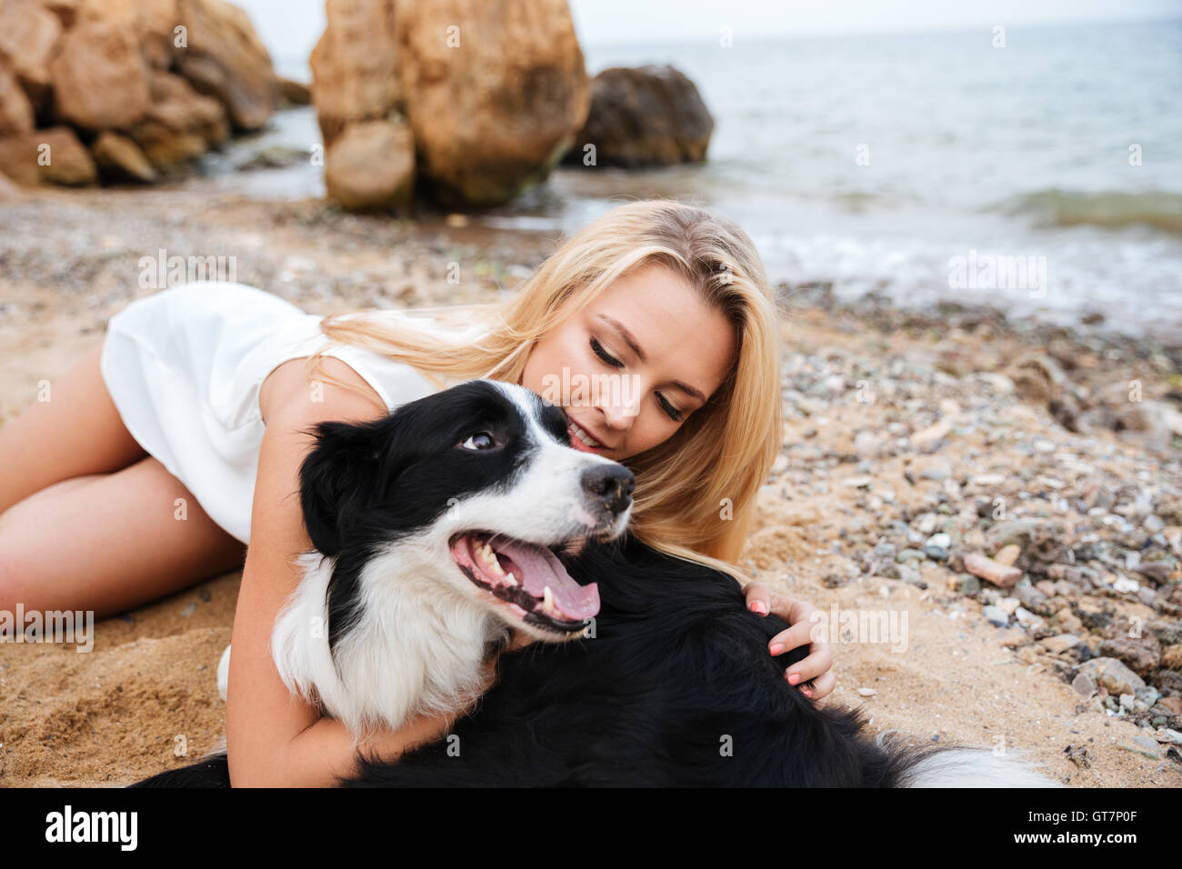 Fröhliche blonde junge Frau liegend und umarmt ihrem Hund am Strand im ... Fröhliche blonde junge Frau liegend und umarmt ihrem Hund am Strand im ...