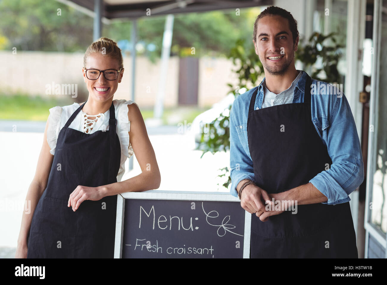 Kellner und Kellnerin mit Speisekarte an Bord vor dem Café stehen ...