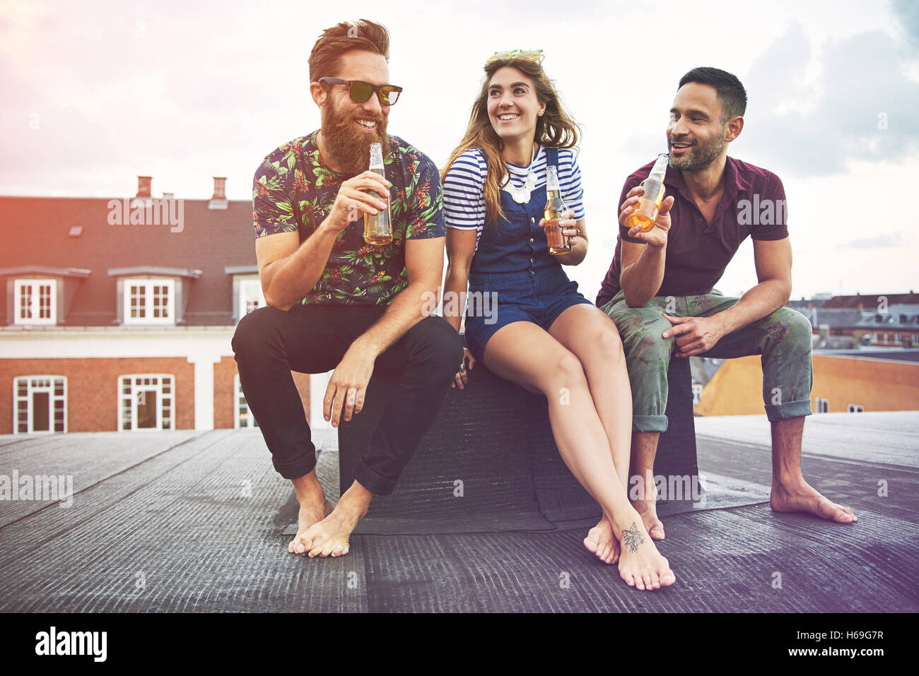 Happy Gruppe von drei Barfuß erwachsene Bier trinken auf dem Dach im ...