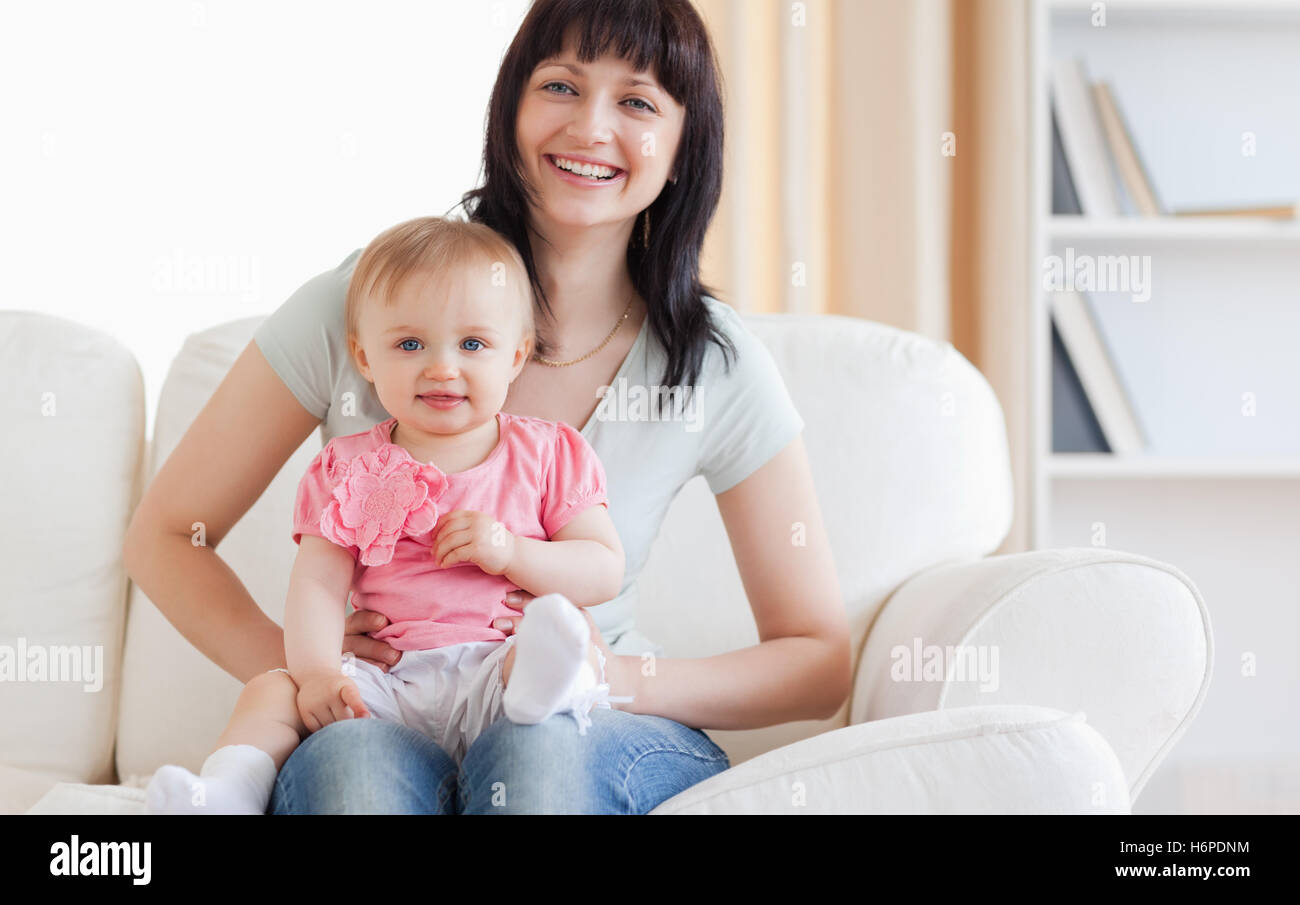 Hübsche Frau hält ihr Baby im Arm beim Sitzen auf einem Sofa im ...