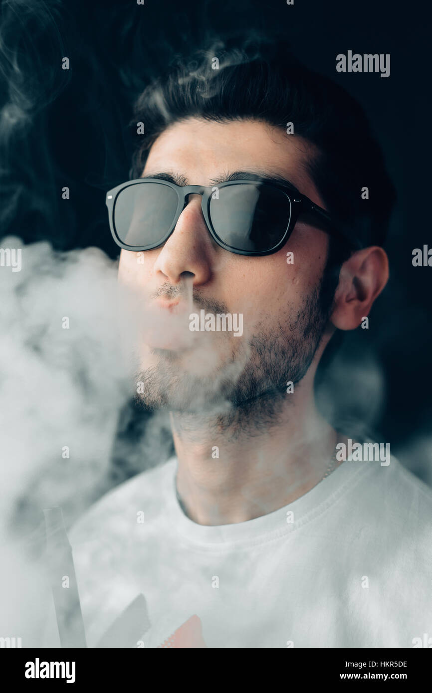 Junge cooler Typ mit Sonnenbrille strahlt eine Rauchwolke. Vertikale ...