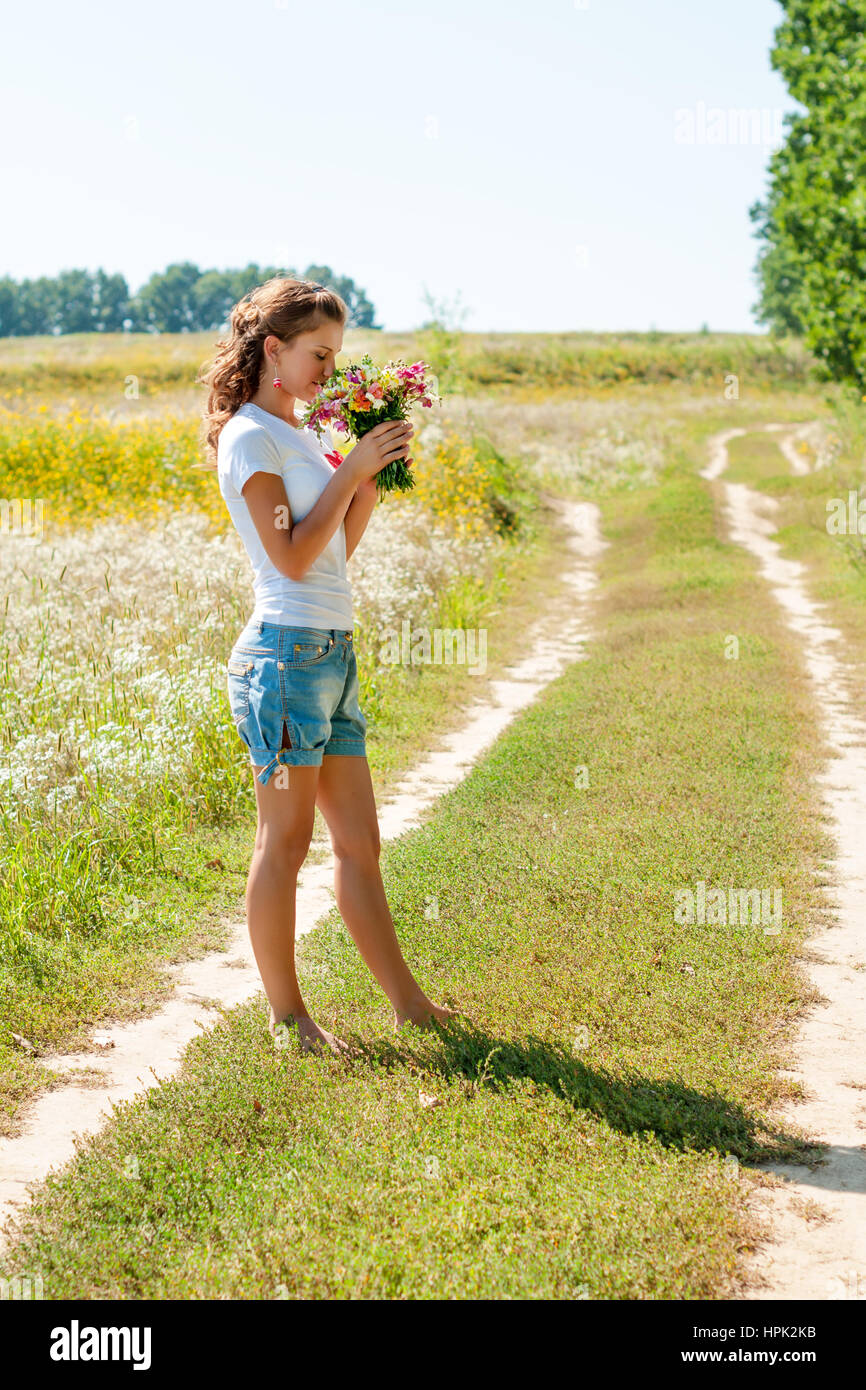 Schöne blonde Mädchen barfuß auf Sommerwiese mit einem Bouquet von ...