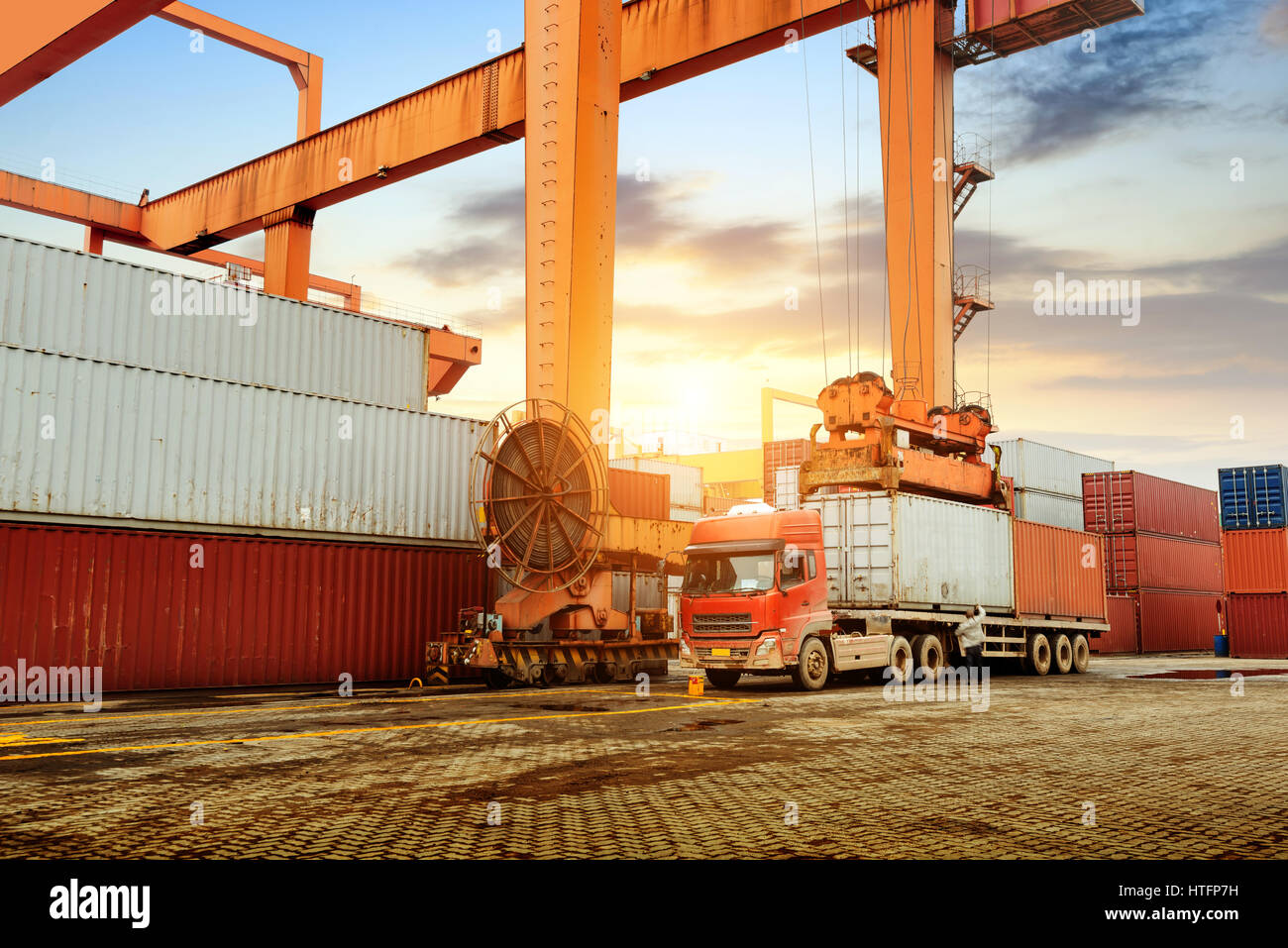 Container-terminal in der Dämmerung, ein großer Kran und LKW beladen ...