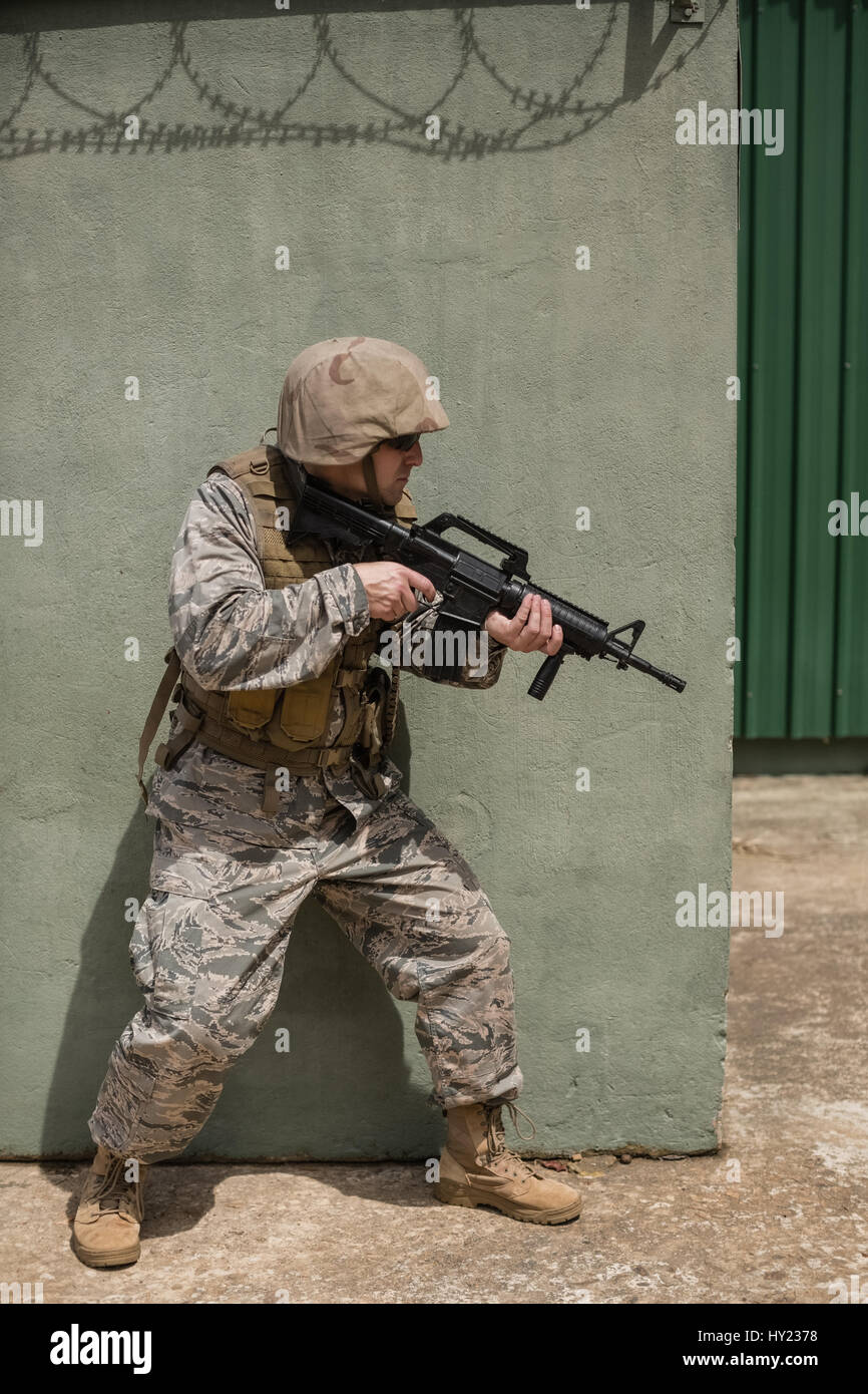 Militärische Soldat mit dem Ziel, mit einem Gewehr gegen die Betonwand ...