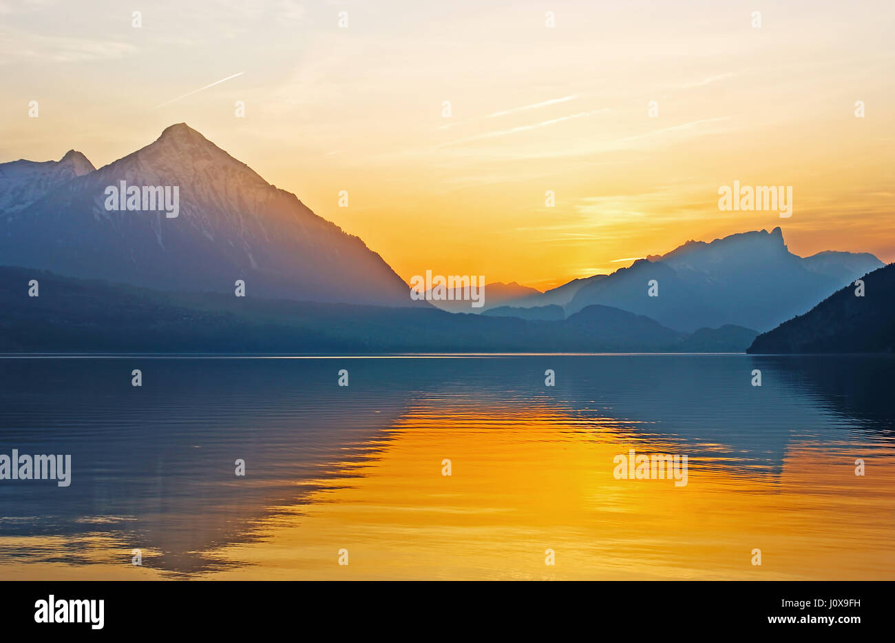 Die Abendsonne versteckt sich hinter den felsigen Alpen und der hellen ...