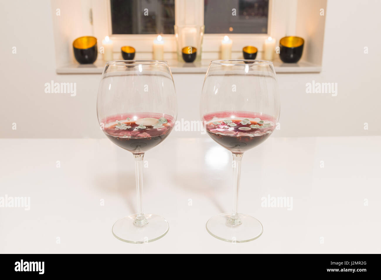 Zwei Gläser mit verschimmelten Rotwein auf weißen Tisch mit weißem ...