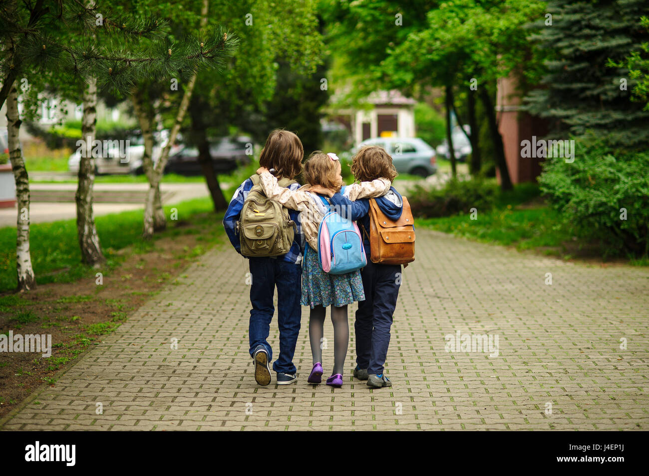 Drei kleine Schülerinnen und Schüler, zwei jungen und Mädchen, gehen in einer Umarmung zur ...