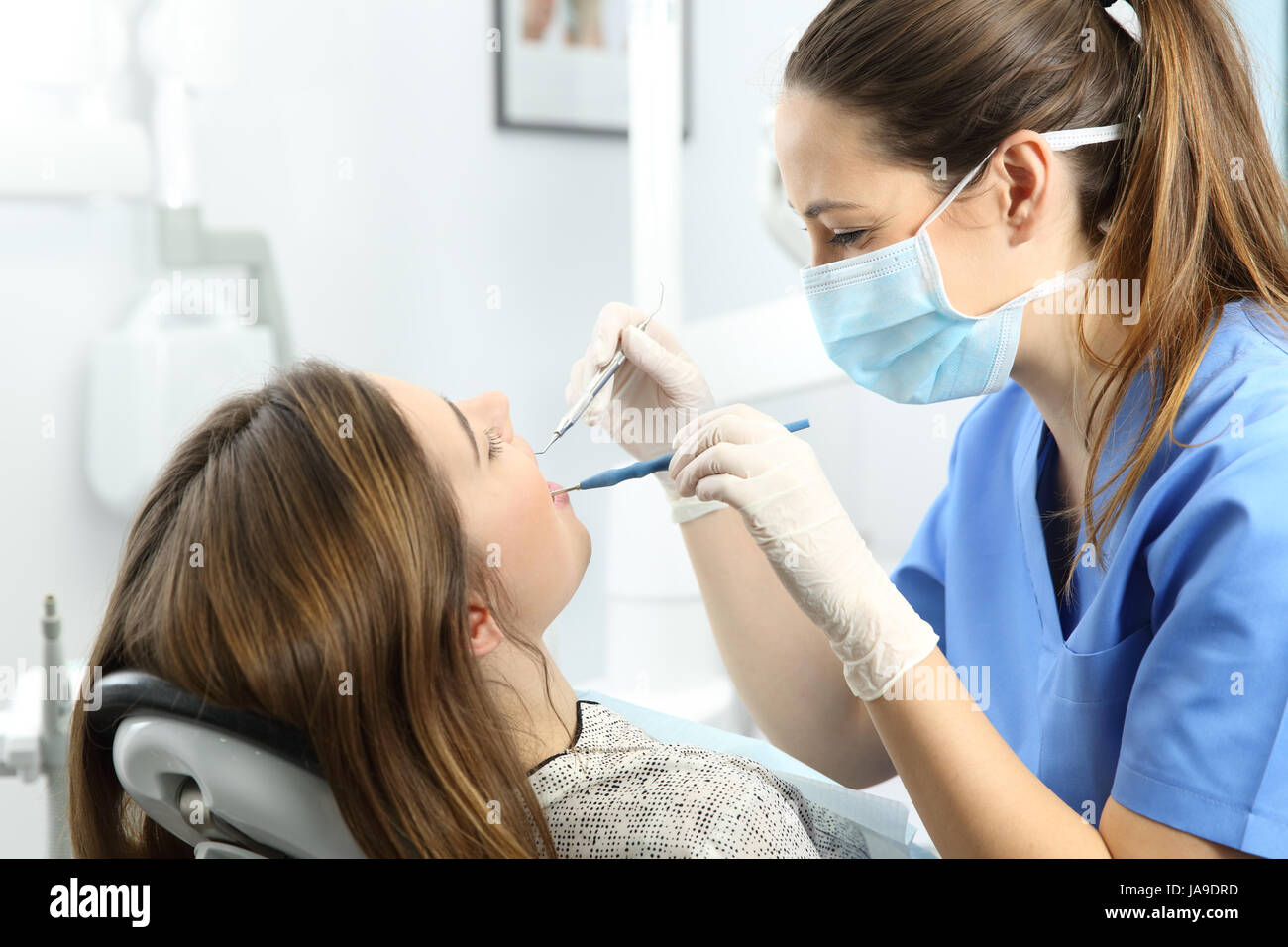 Zahnarzt, tragen von Handschuhen Maske und blaue Uniform, die Untersuchung eines Patienten Zähne ...