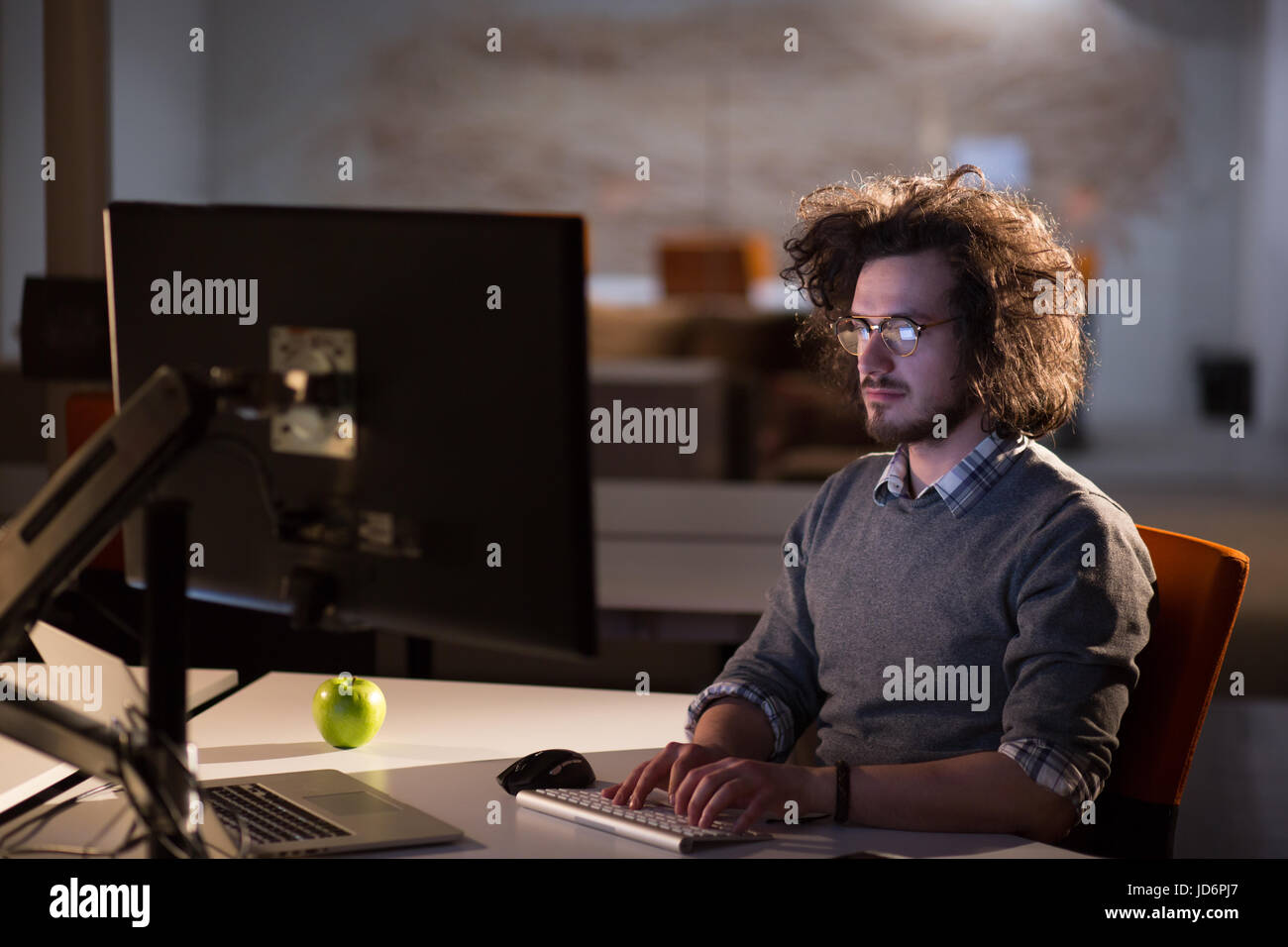 Junger Mann nachts im dunklen Büro am Computer arbeiten. Der Designer ...