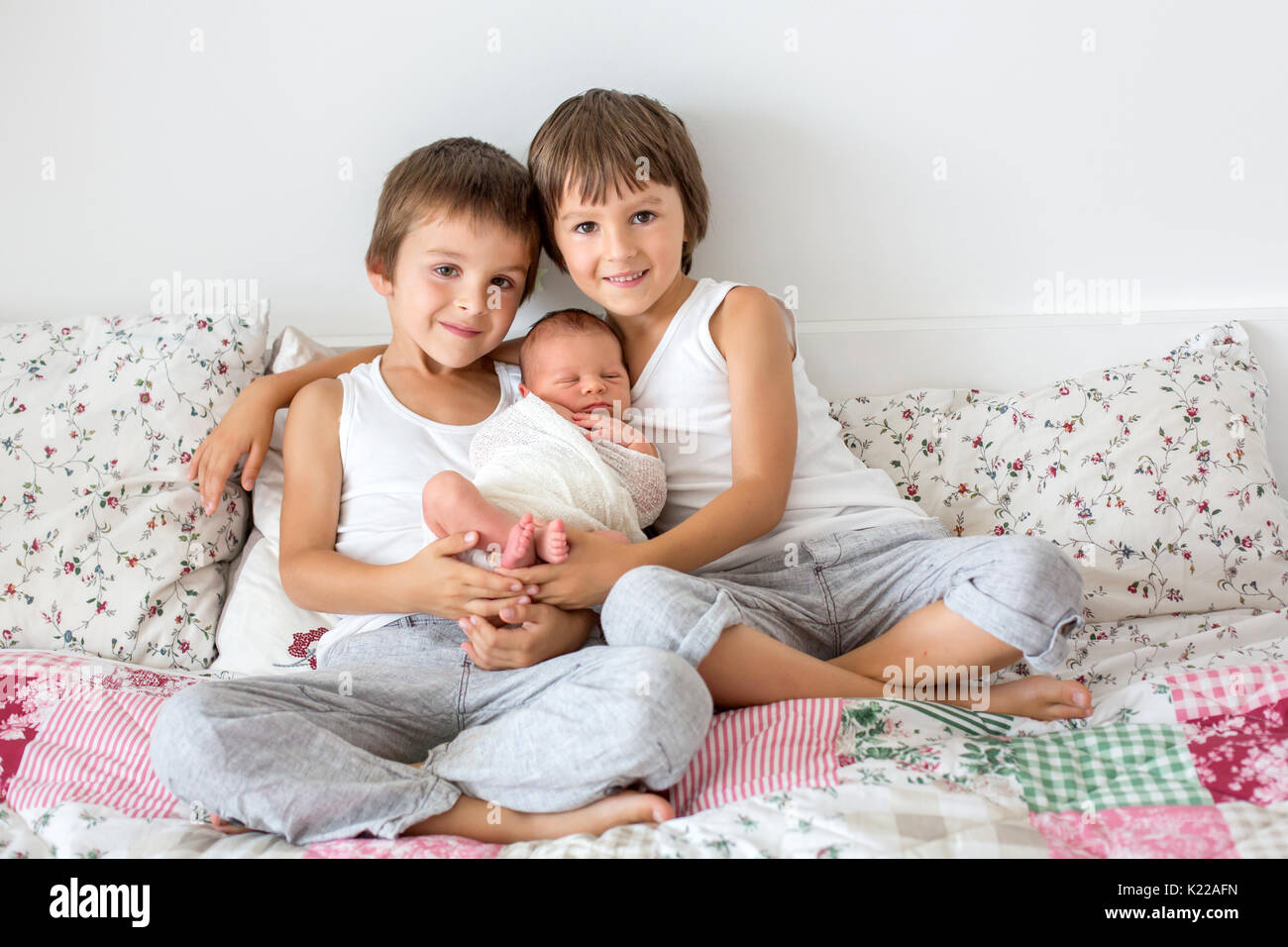 Zwei Kinder, Kleinkind und seinen großen Bruder, umarmen und küssen ihre neugeborenen Bruder zu ...