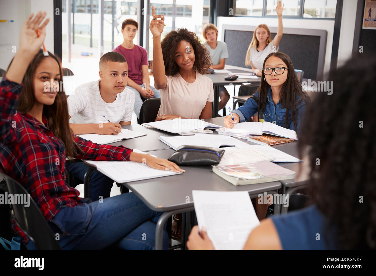 High School Kids heben die Hände, Lehrer an Ihrem Schreibtisch sitzen ...
