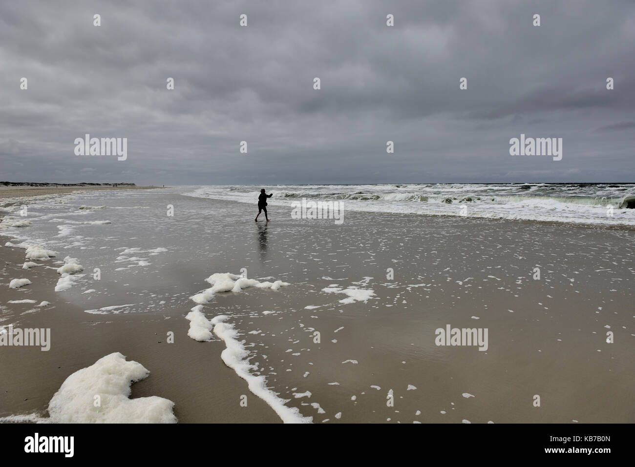 Der Strand von Terschelling mit Schaum und Silhouette der Person, die ...