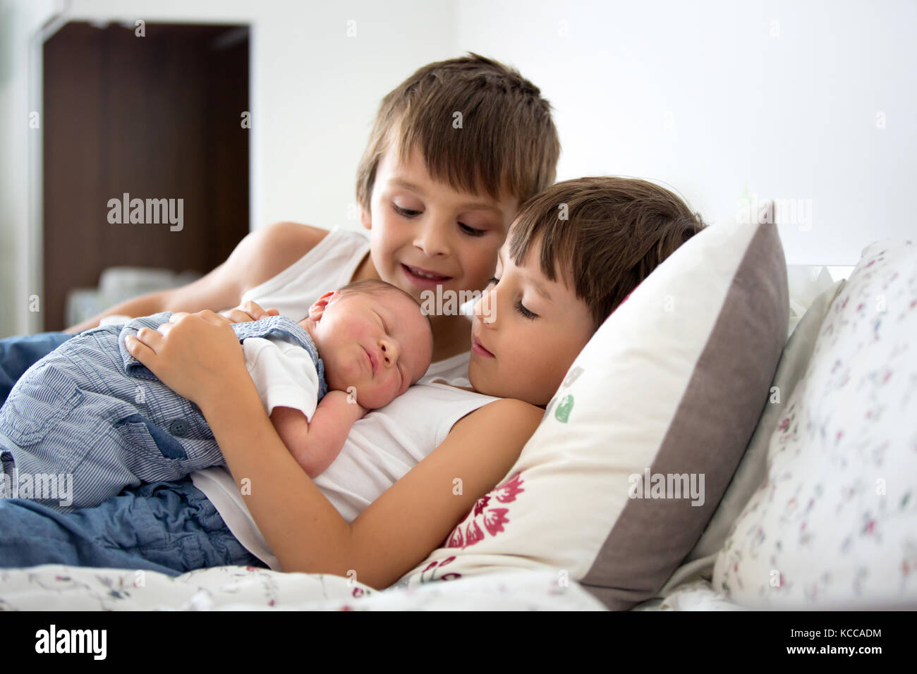 Zwei Kinder, Kleinkind und seinen großen Bruder, umarmen und küssen ihre neugeborenen Bruder zu ...