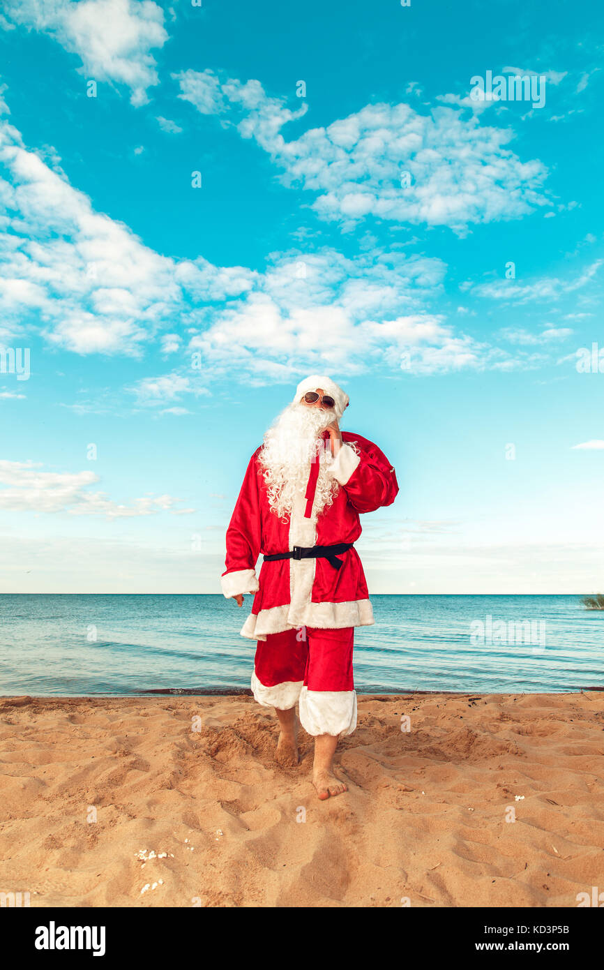 Santa Claus mit einem Beutel der Geschenke am Strand. Das Symbol für ...