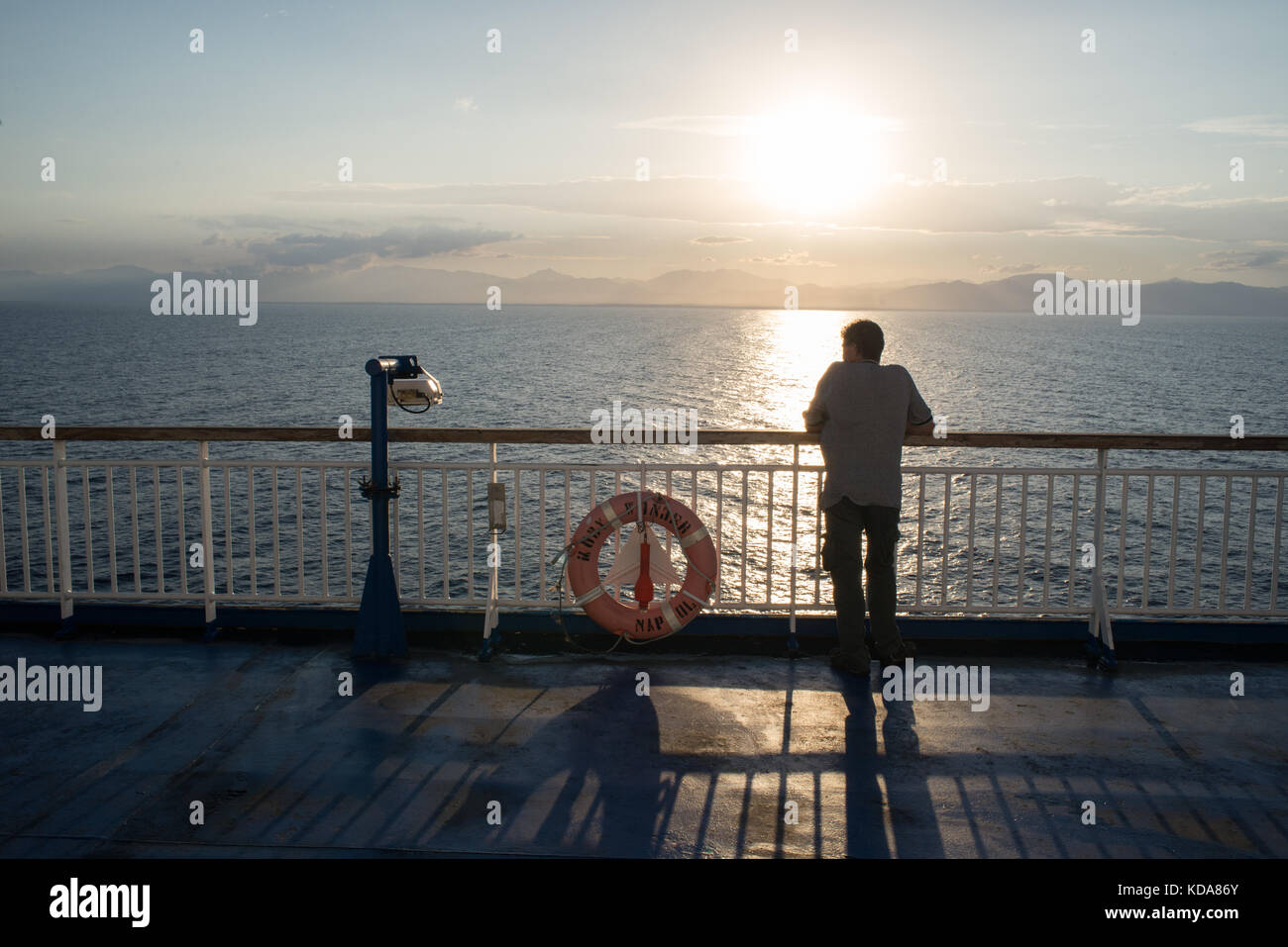 Ein Mann sieht, wie die Sonne am Horizont auf dem Meer beim Segeln im ...