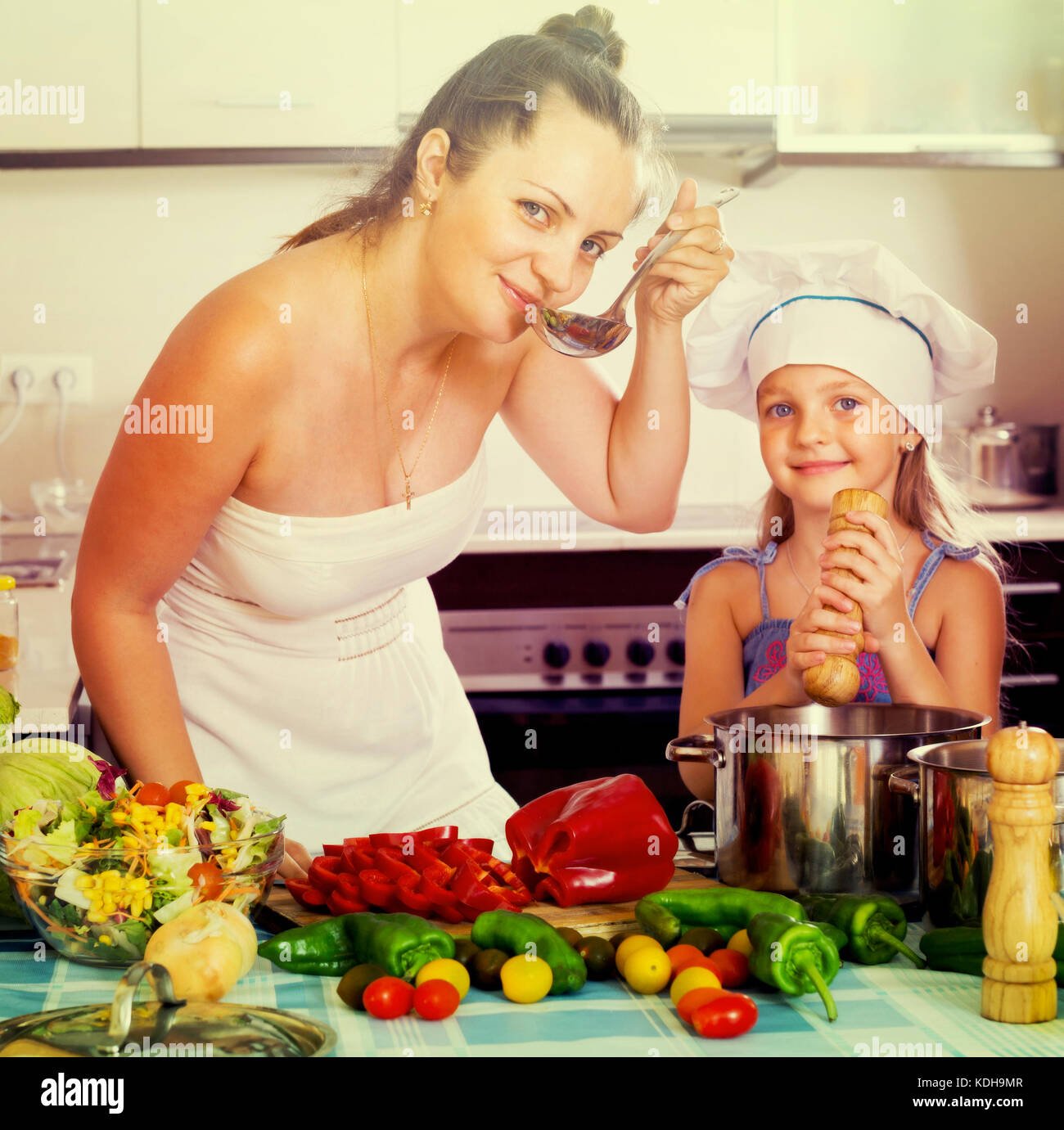 Lächelnd süße kleine Mädchen mit mom Schneiden von Gemüse für die Suppe ... Lächelnd süße kleine Mädchen mit mom Schneiden von Gemüse für die Suppe ...