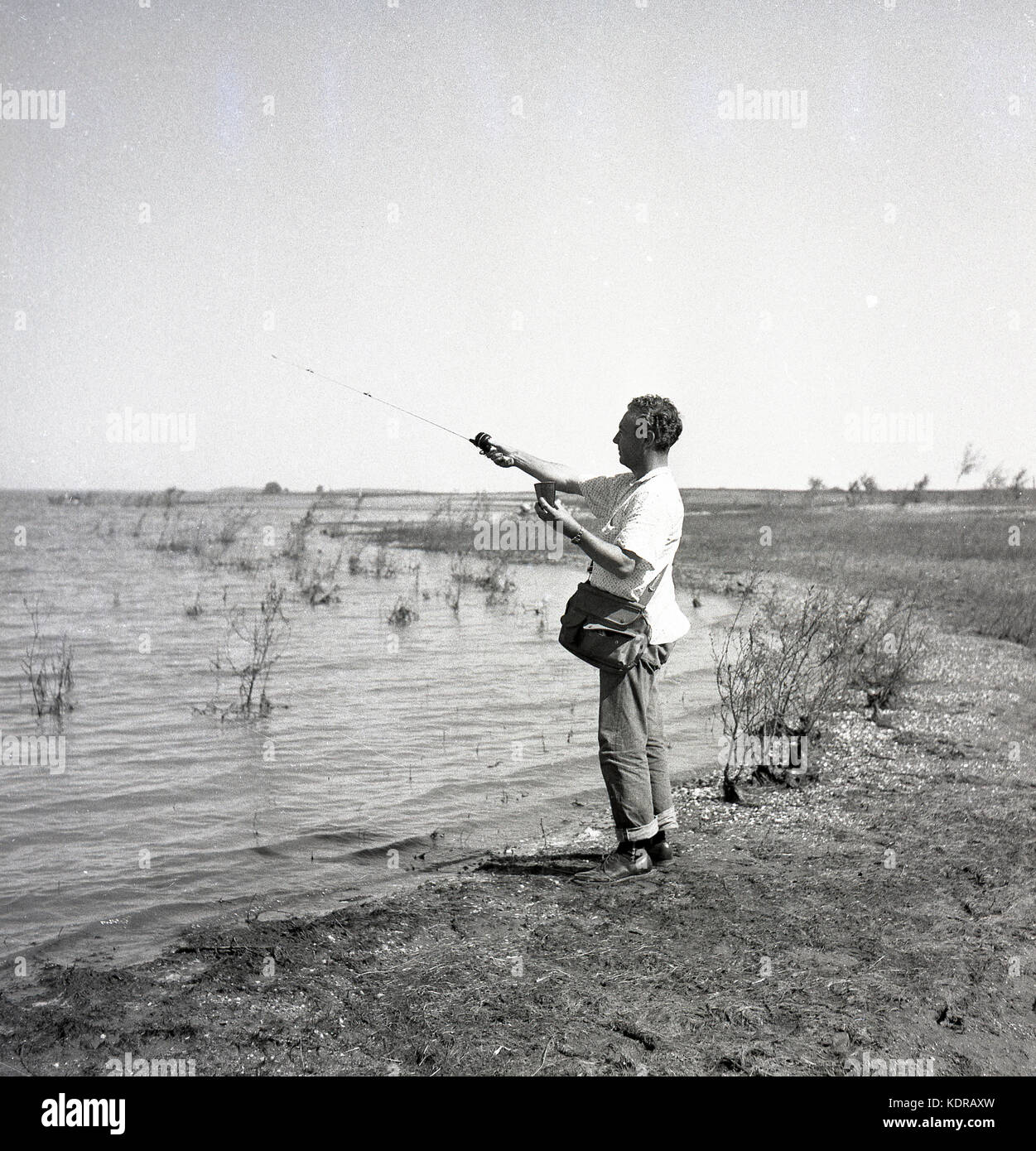1950, historische, Mann in Jeans und eine satchel Angeln im See, stehen ...