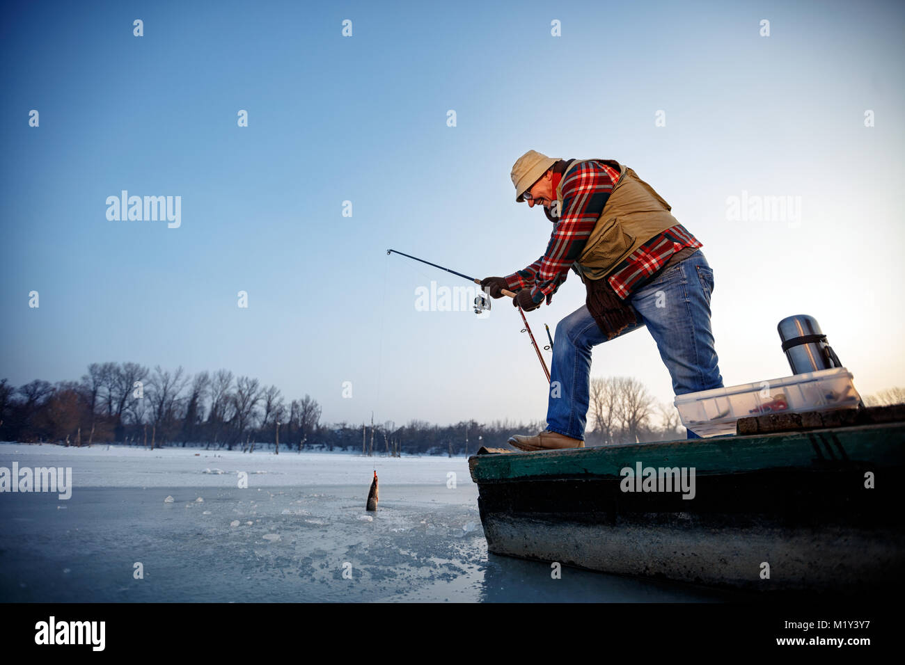 Lächelnd alter Fischer fangen Fische auf dem gefrorenen Fluss im Winter ...