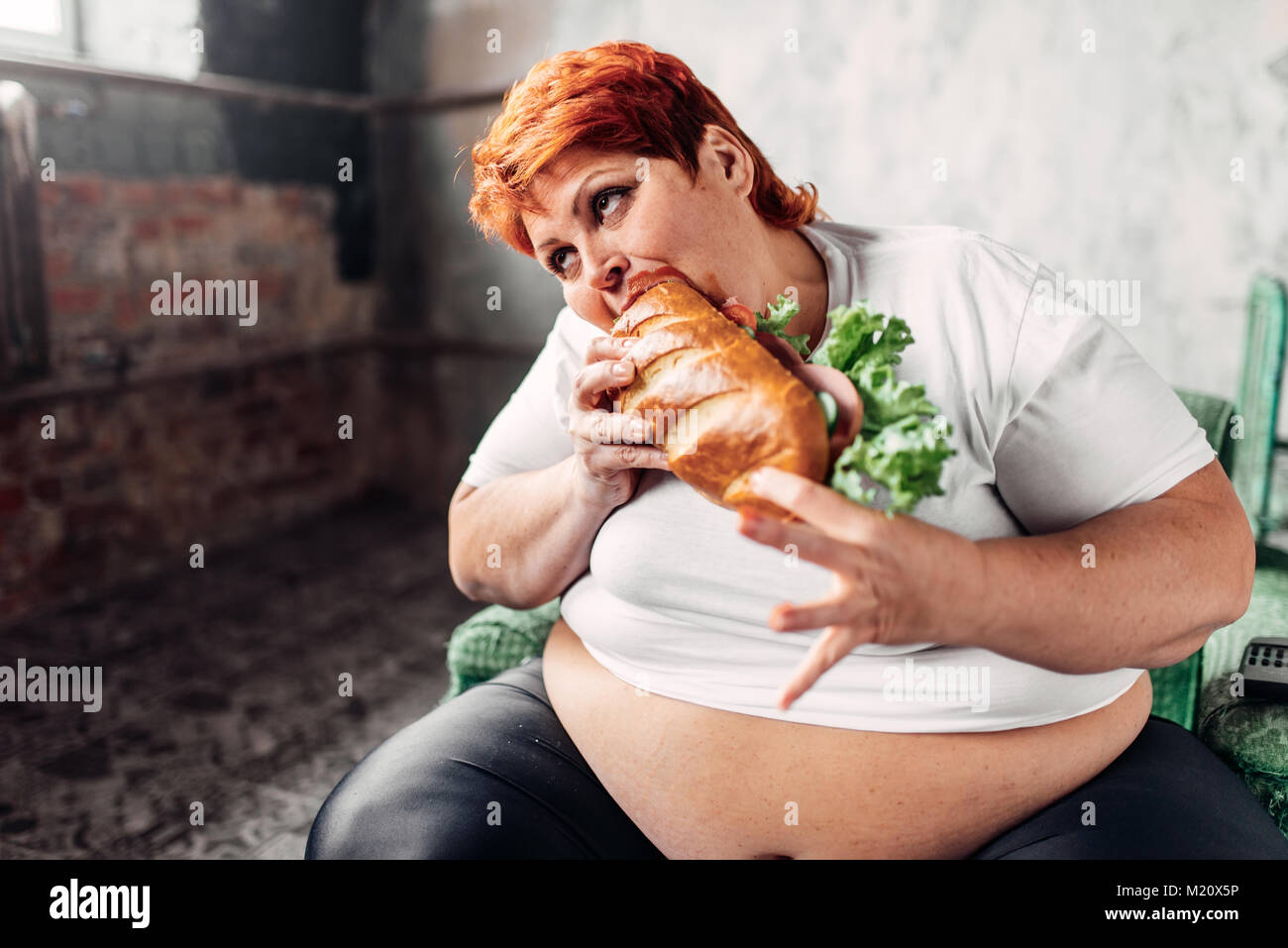 Fette Frau sitzt in einem Sessel und isst Sandwich, bulimic und ...