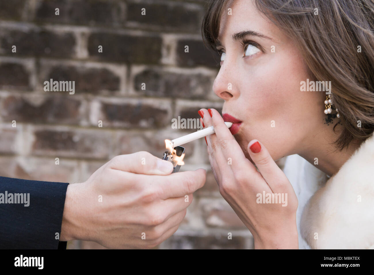 Des Menschen Hand eine Zigarette für eine brünette Frau mit roten ...