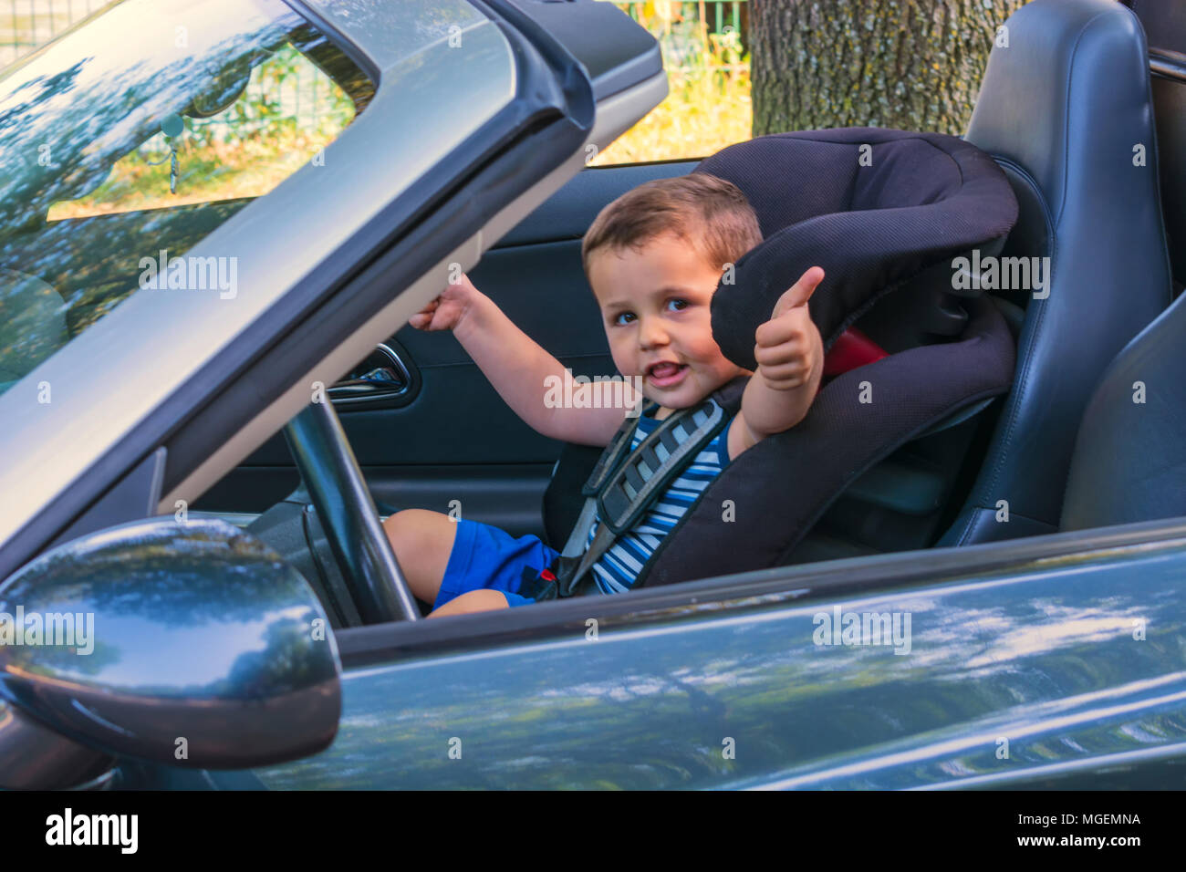 Glückliches lachendes Kind in einem Cabrio sitzt im Auto Kindersitz und ...
