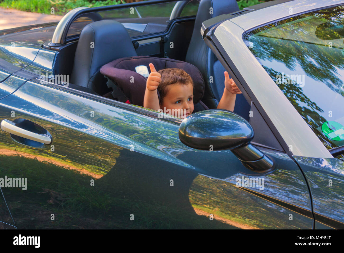 Glückliches lachendes Kind in einem Cabrio sitzt im Auto Kindersitz und ...