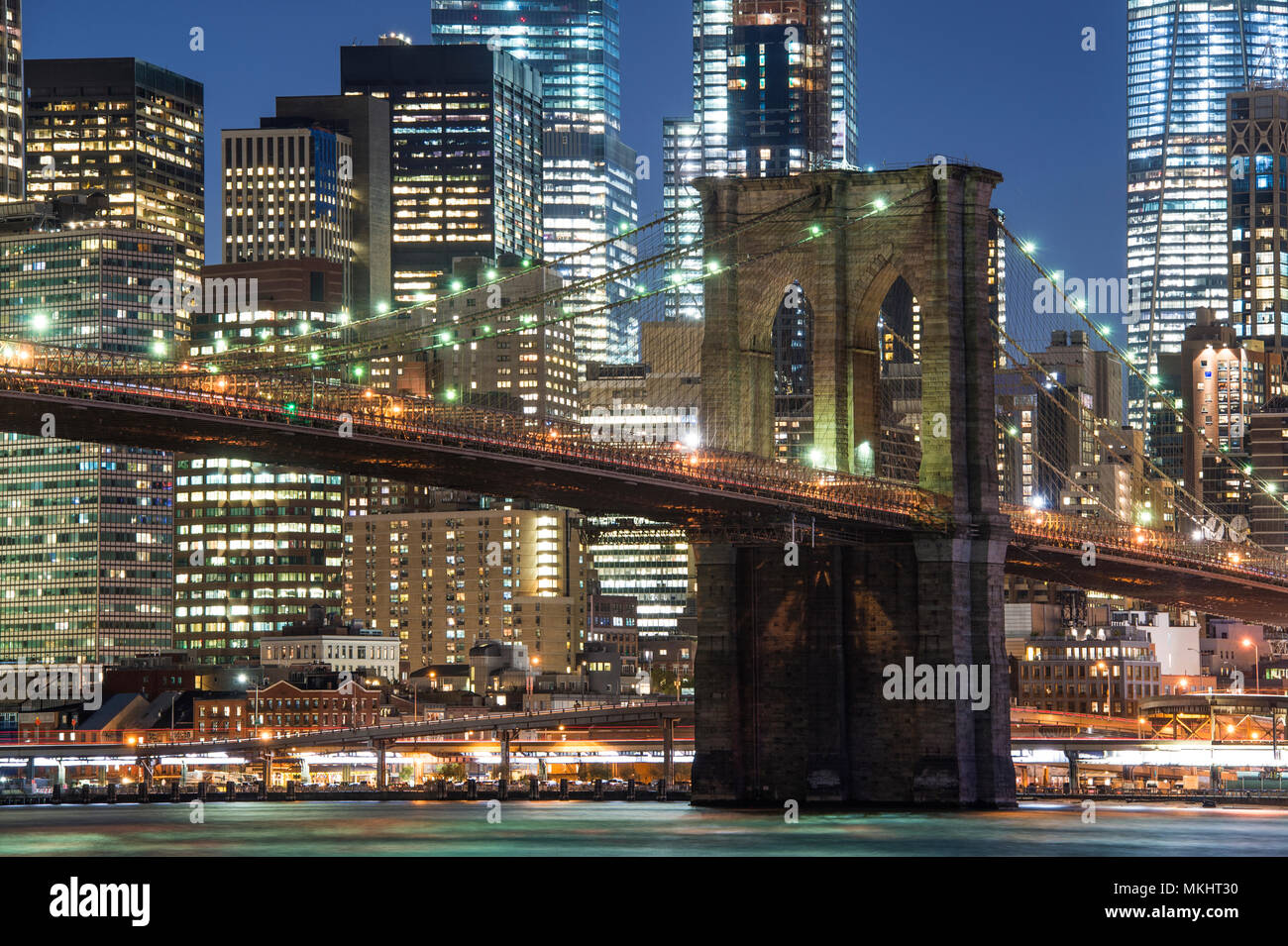 Brooklyn Bridge und die beleuchtete Skyline von Manhattan am Abend mit blauem Himmel und glatte ...