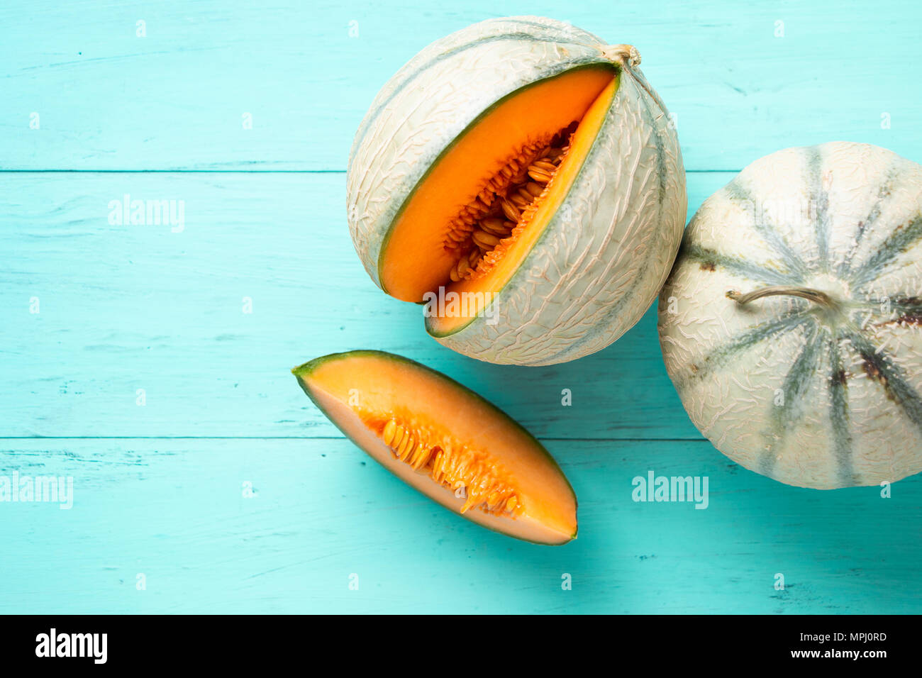 Zwei melone Melonen und eine Scheibe auf ein Aquamarin Holzbohlen ...
