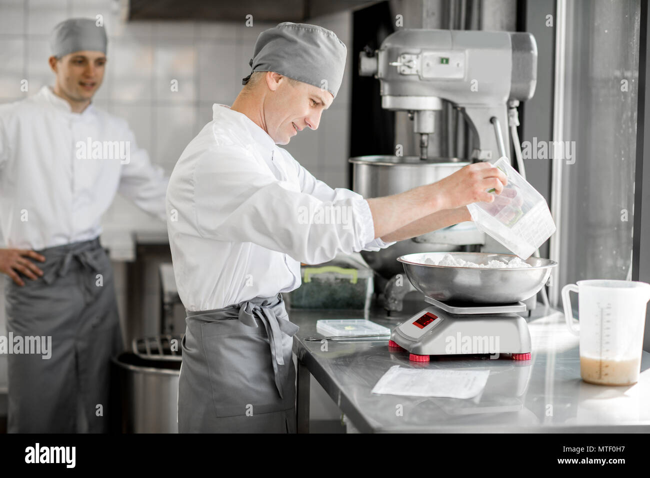 Zwei stattliche männliche Konditoren in Uniform wiegen Zutaten zum ...