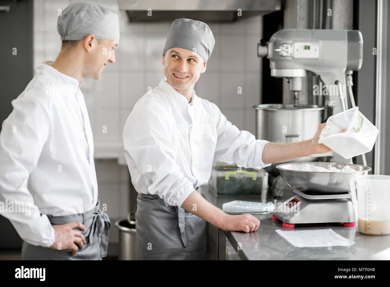 Zwei stattliche männliche Konditoren in Uniform wiegen Zutaten zum ...