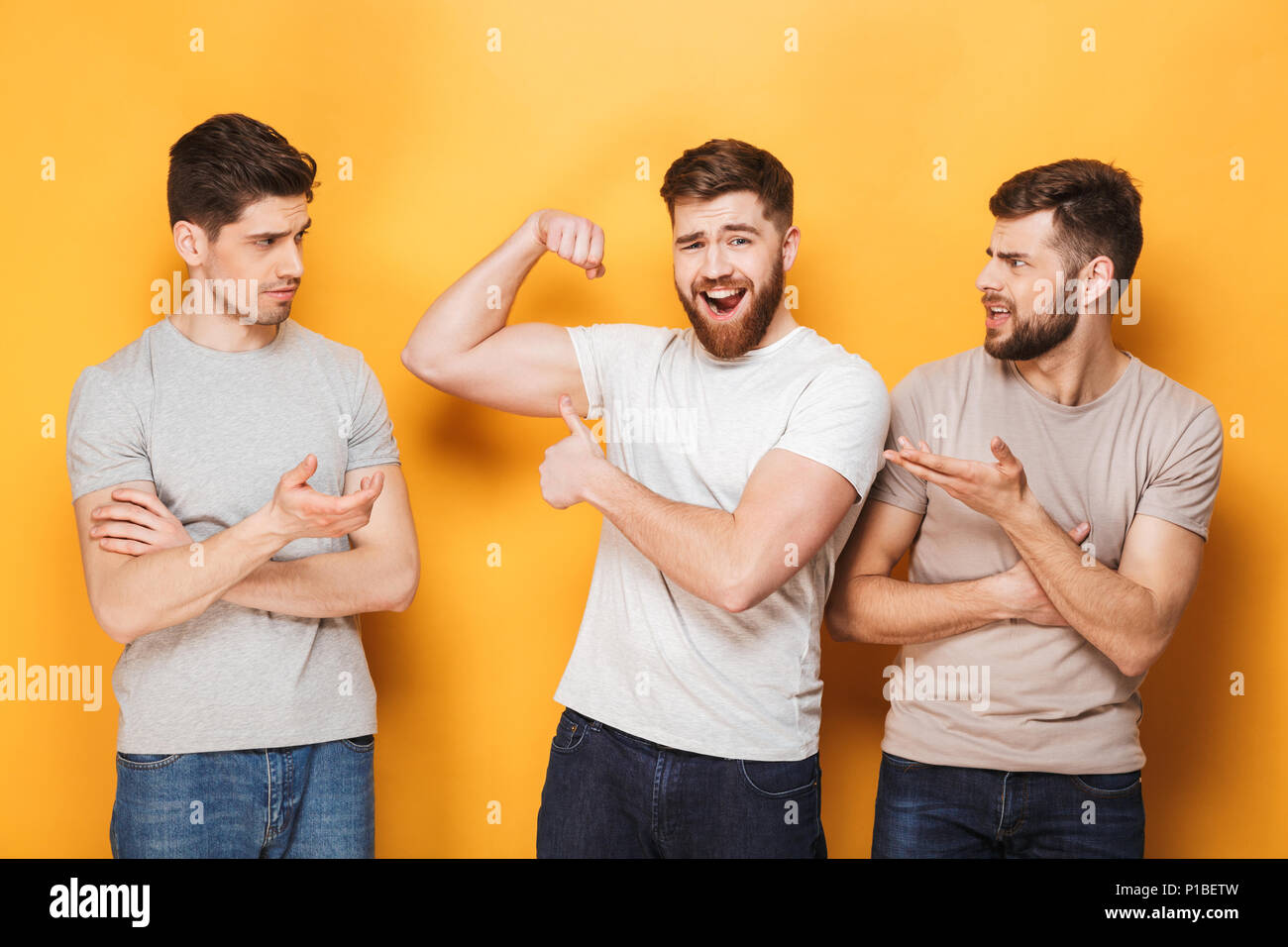 Zwei junge Männer neidisch Blick auf Ihre männlichen Freund über Gelb ...