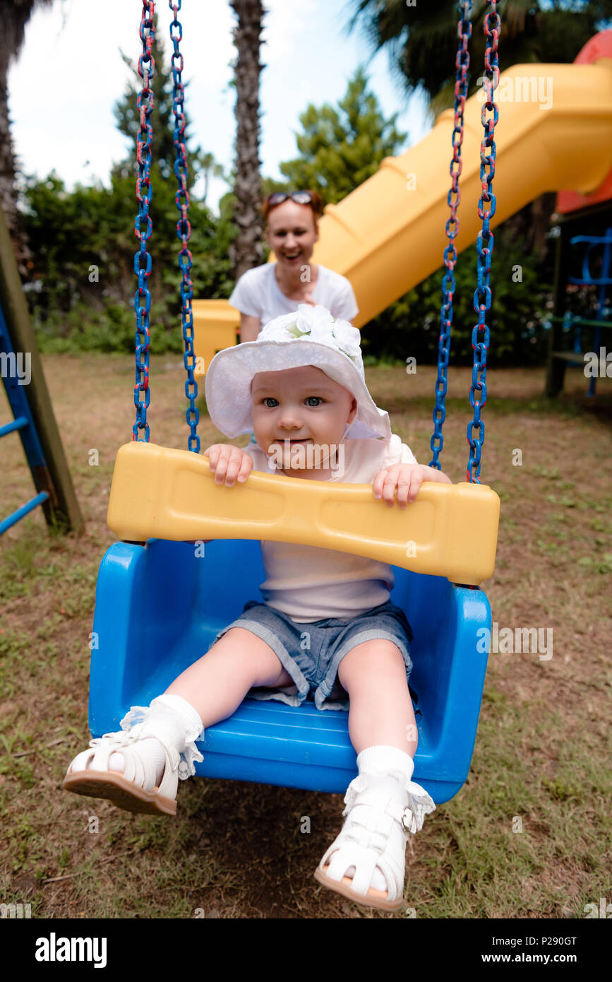 Das Mädchen lacht und schiebt das Kind in der blauen Schwingen auf dem ...