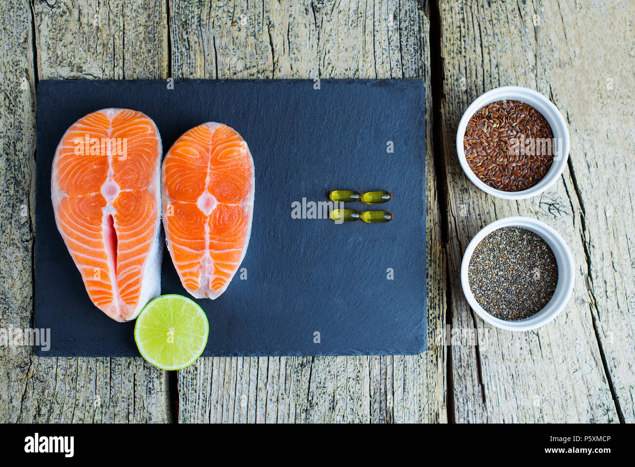 Zwei Lachs Steaks liegen auf einem schwarzen Brett und neben Es gibt ...