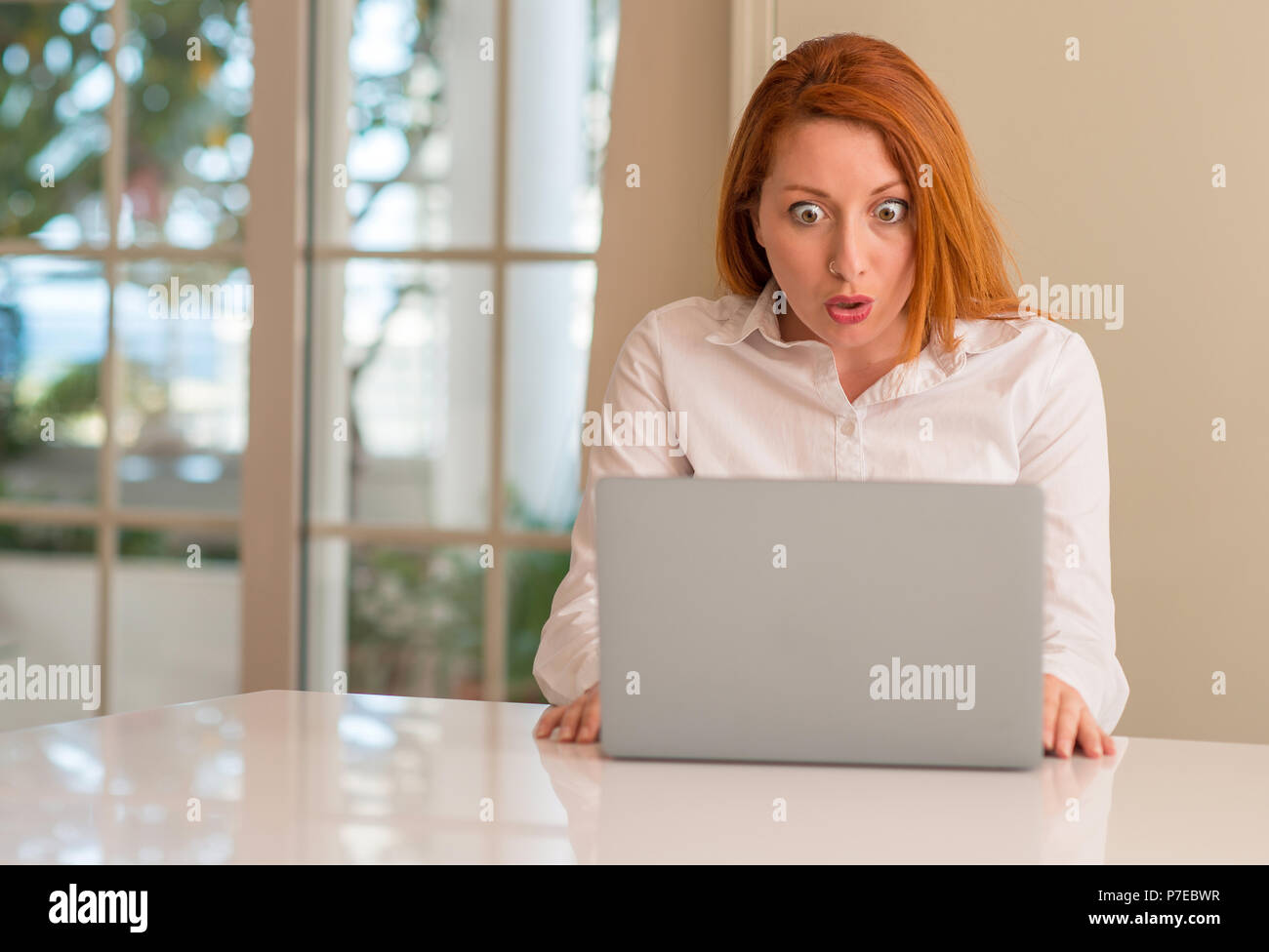 Rothaarige Frau mit Computer Laptop zu Hause Angst im Schlag mit einer ...