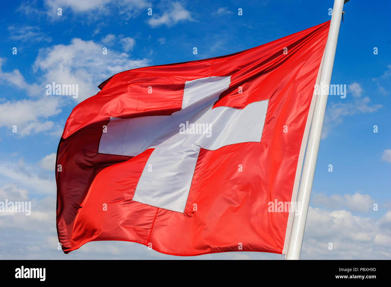 Die schweizer Fahne flattert im Wind vor einem blauen Himmel mit Wolken ...